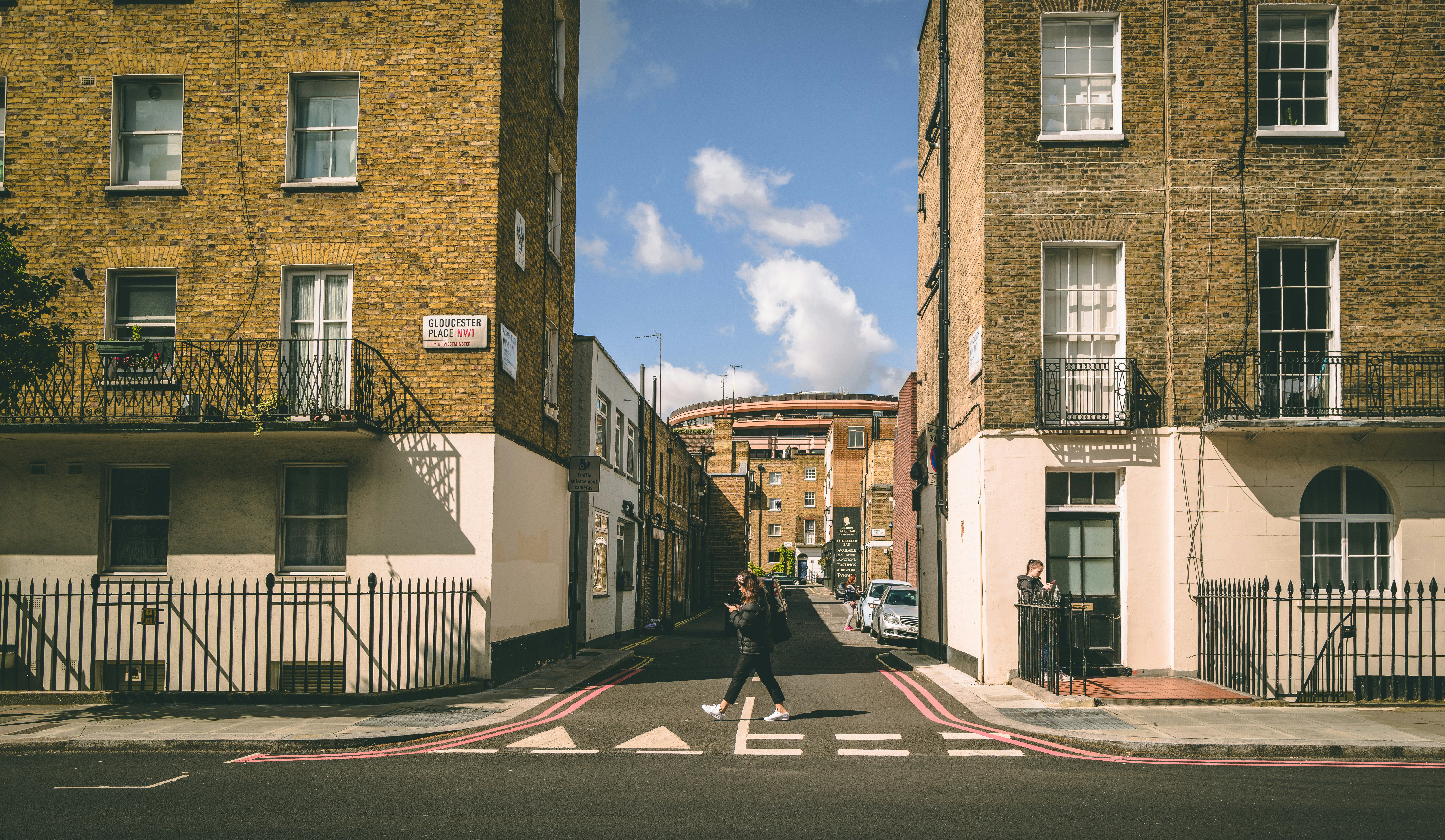 Pedestrian walking across a crosswalk between historic brick buildings on a sunny day.
