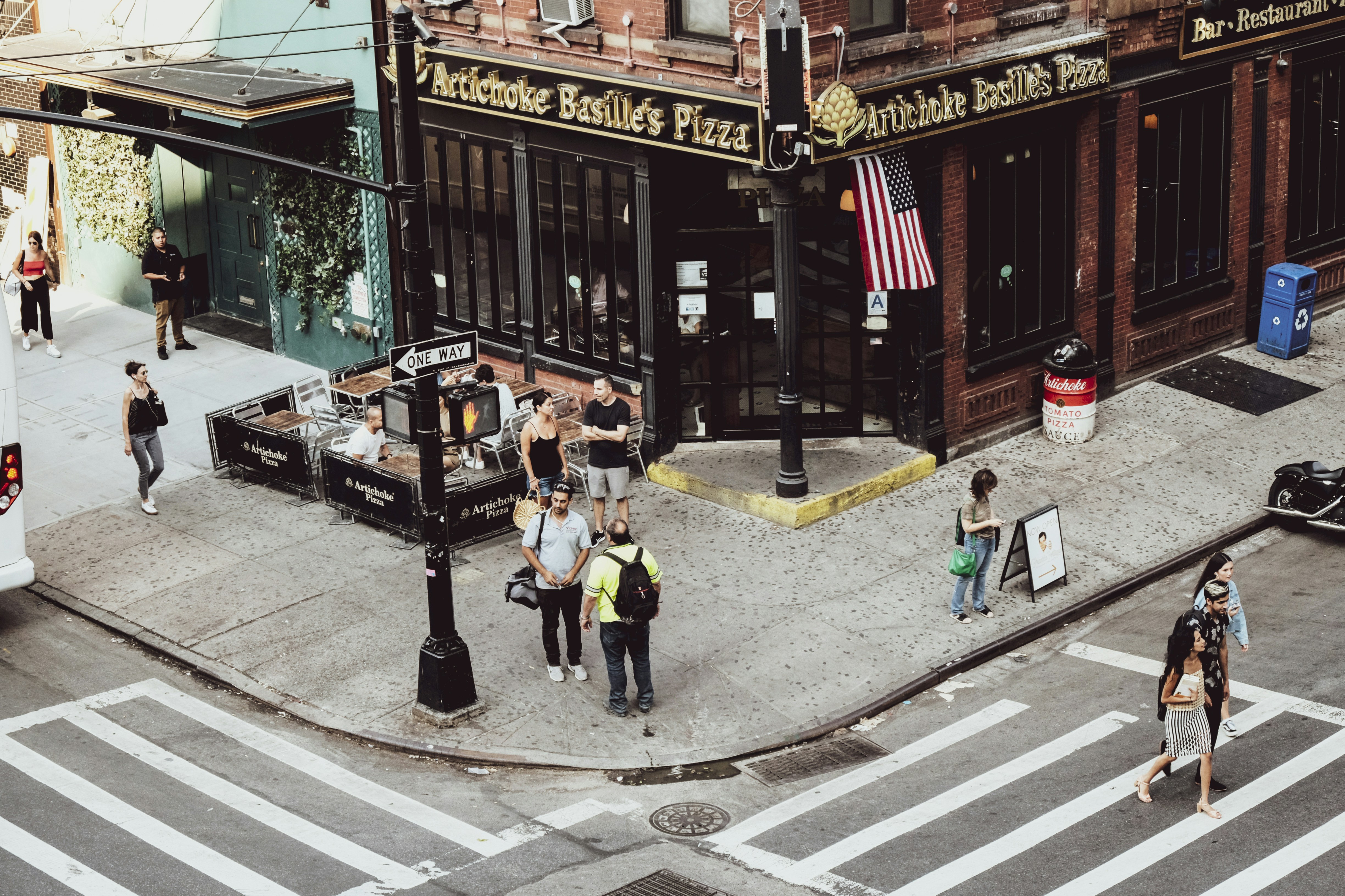 Crowd of people socializing outside Artichoke Basille's Pizza in a bustling city street scene.