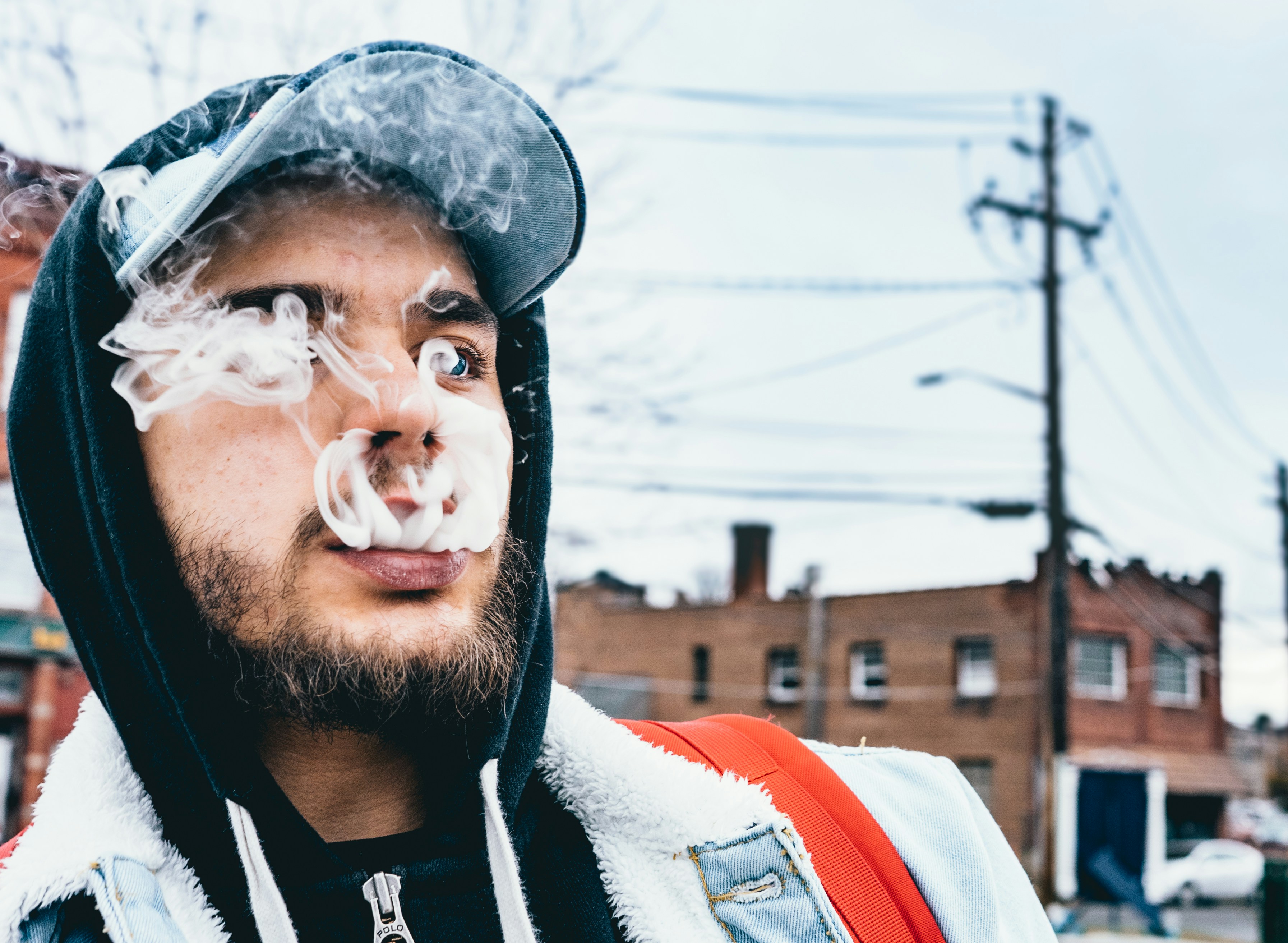 Young man exhaling smoke against an urban backdrop, capturing a moment of relaxed defiance.