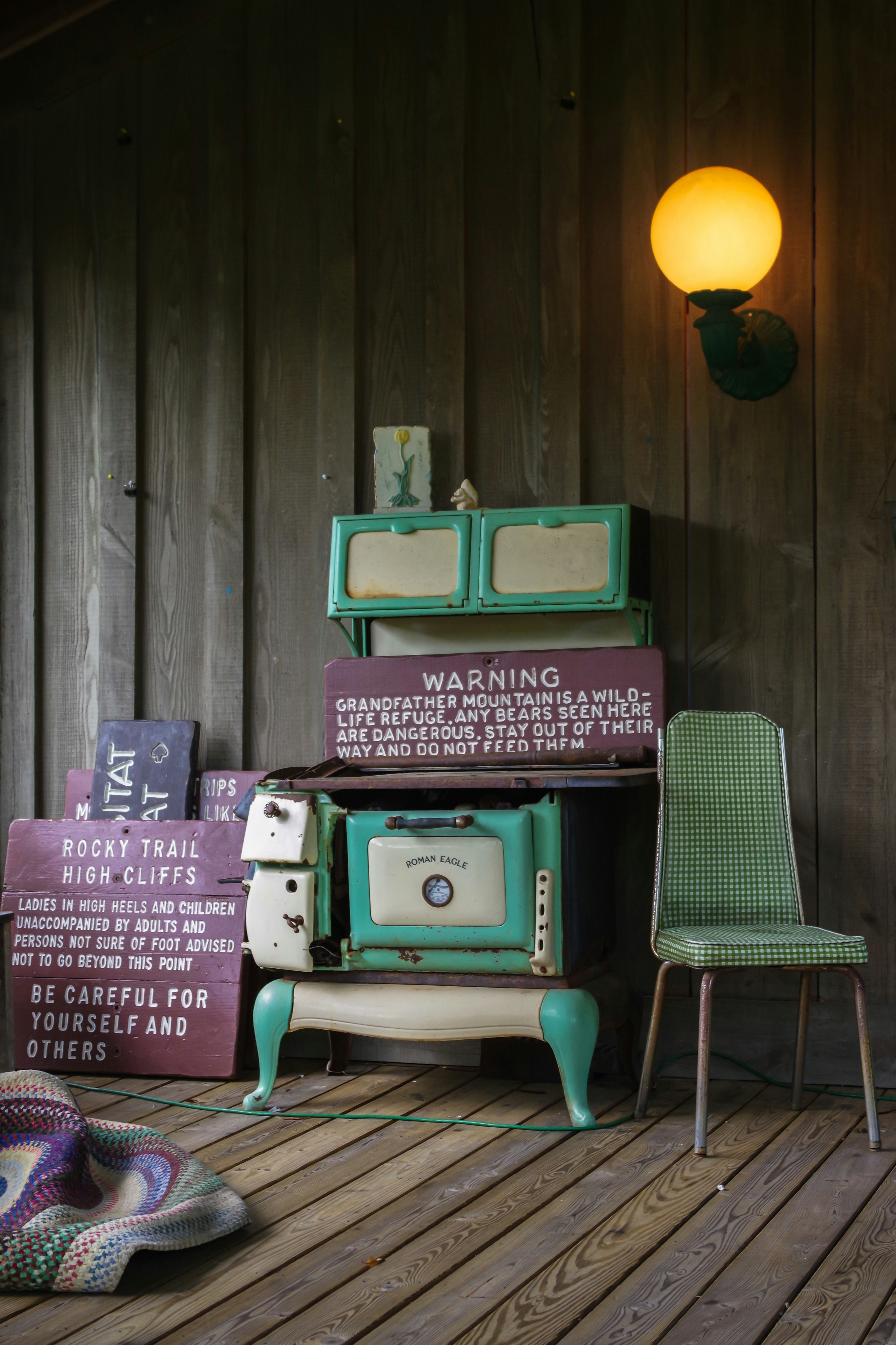 Vintage stove adorned with warning signs and a green chair in a rustic wooden setting. The warm glow of a wall-mounted light adds to the cozy atmosphere.