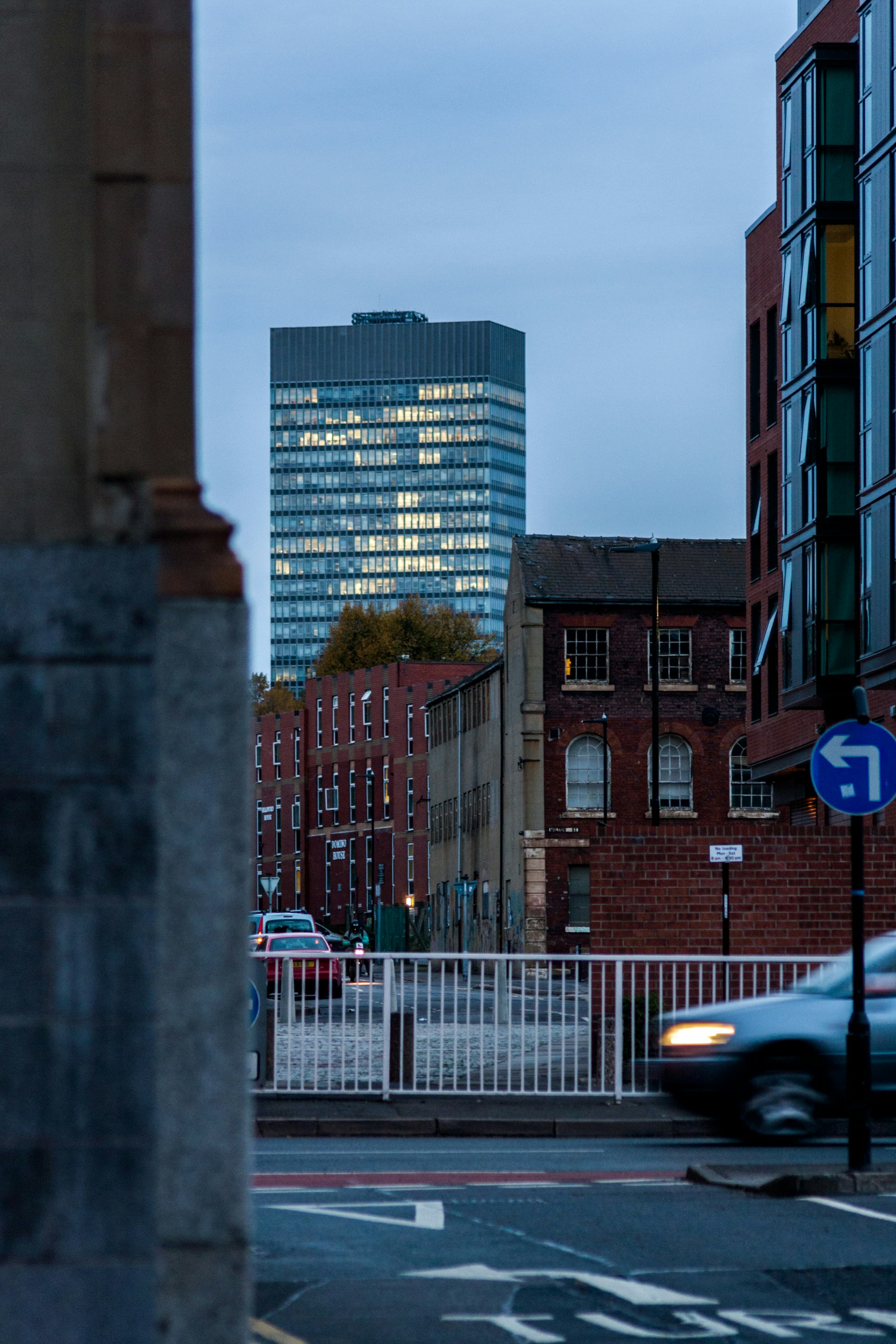 A sleek modern building reflects the twilight sky, surrounded by historic brick structures in an urban setting.