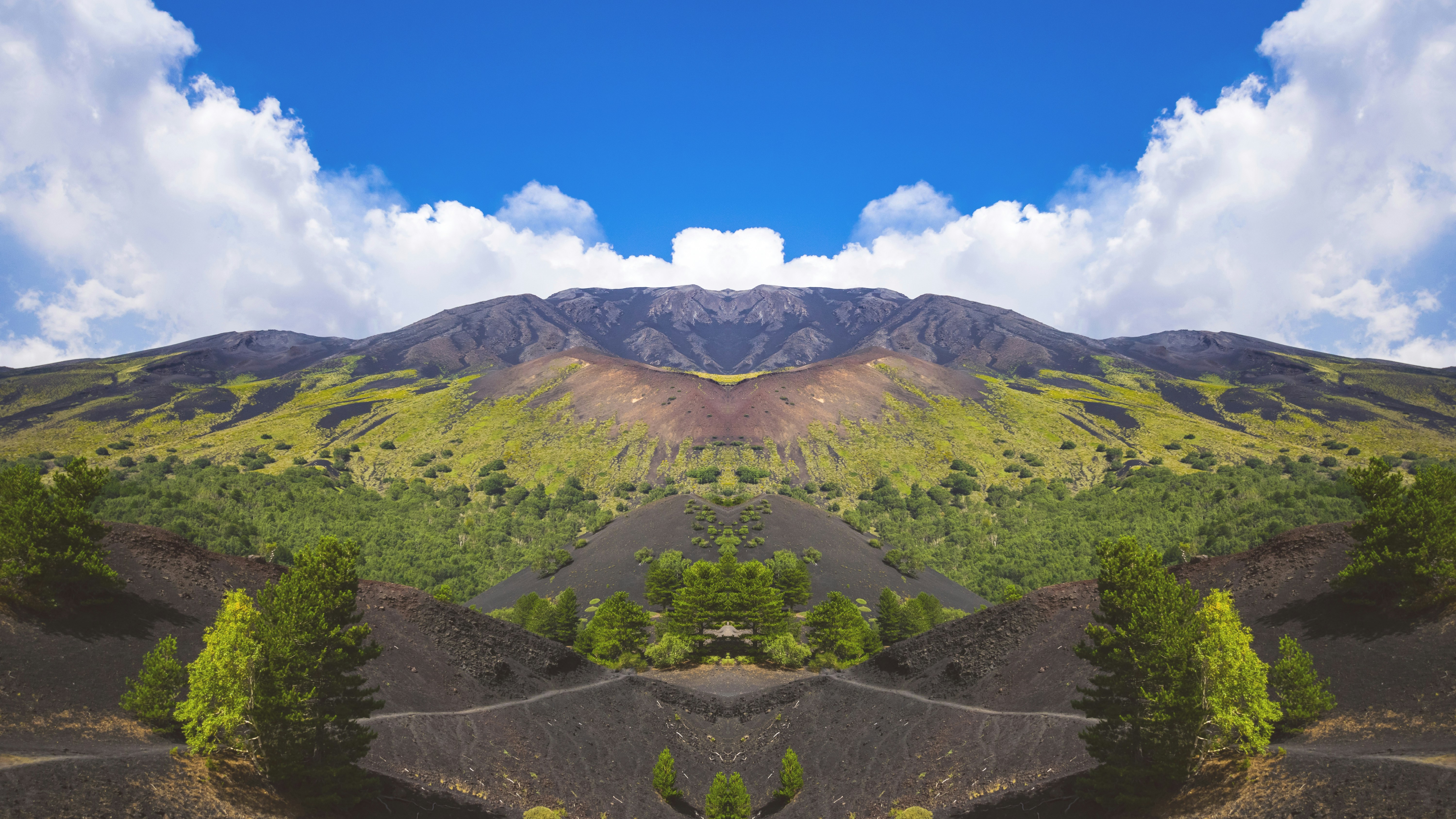 Symmetrical landscape with vibrant green slopes and a deep blue sky framed by fluffy clouds.