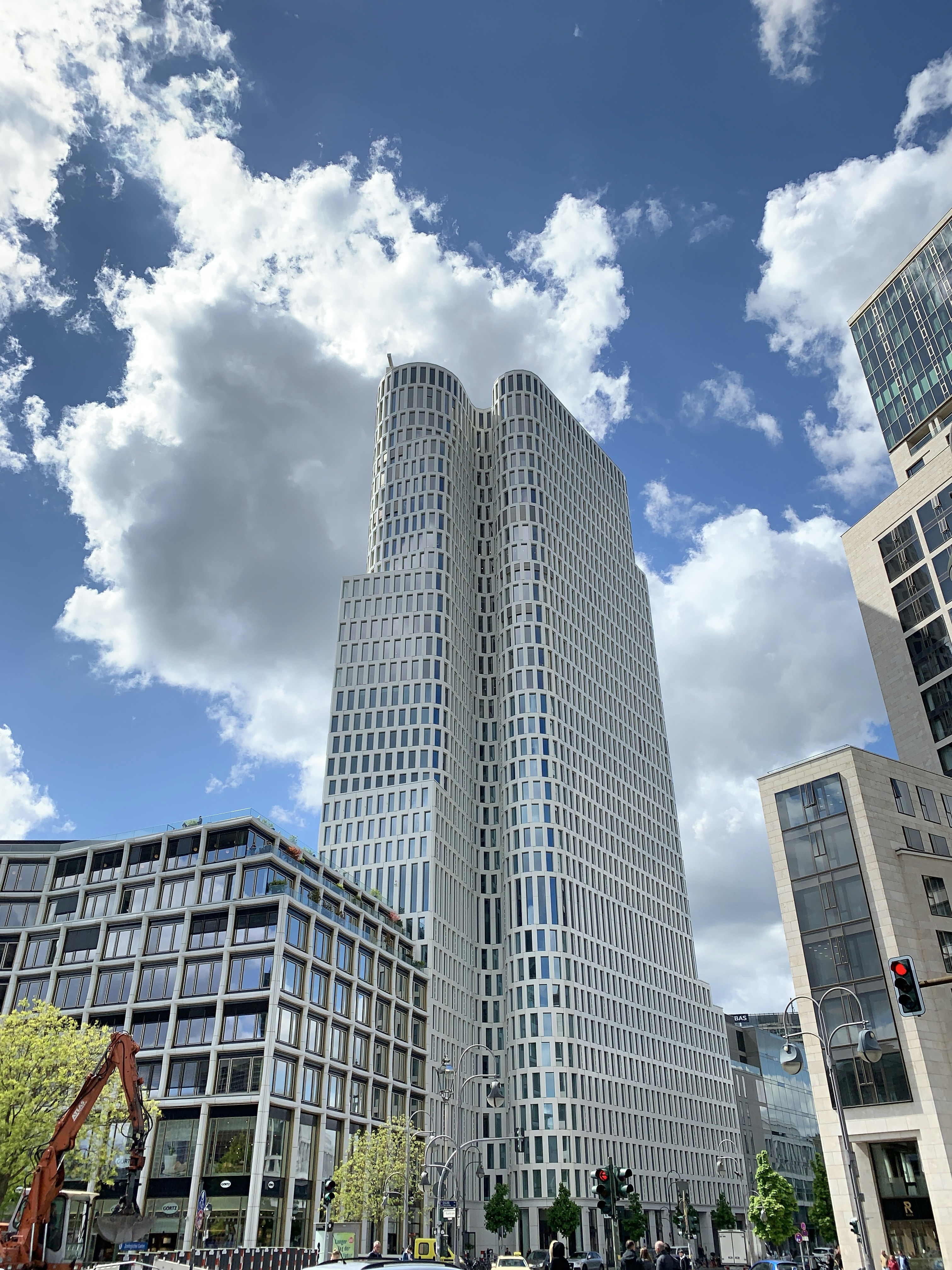 Tall modern skyscraper with curved design under a vibrant blue sky with scattered clouds.