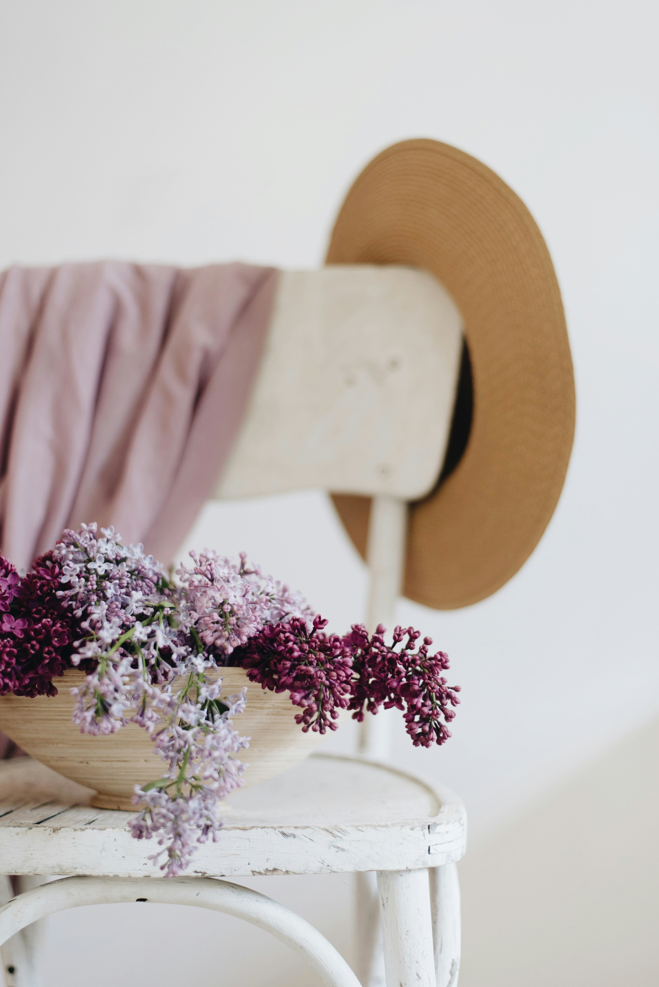 Lilac Bouquet on a Weathered Chair: Quiet Light, Soft Drapery, and a Straw Hat