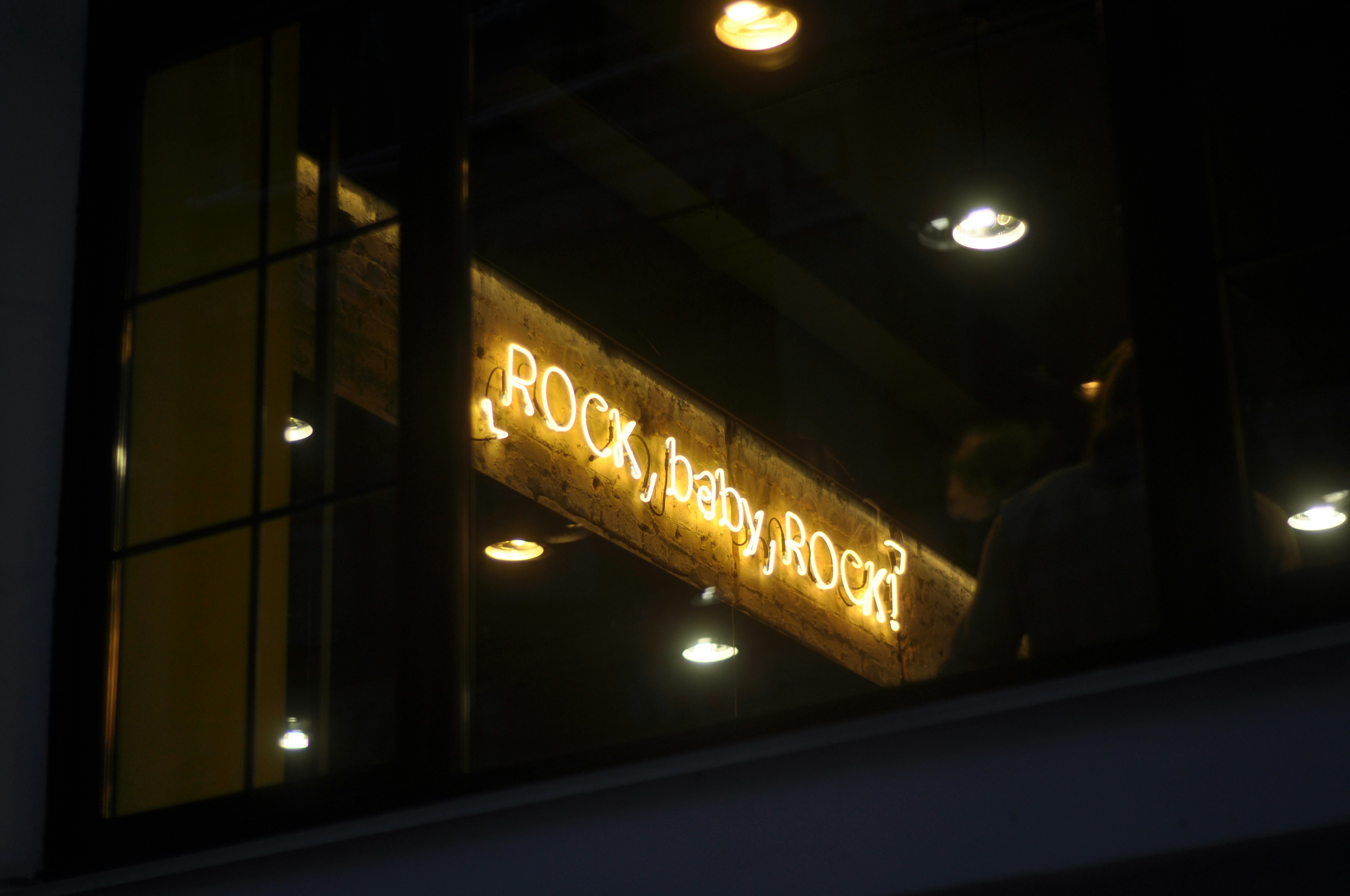Neon sign reading 'ROCK, baby, ROCK!' illuminates a dimly lit interior, reflecting the vibrant nightlife atmosphere.