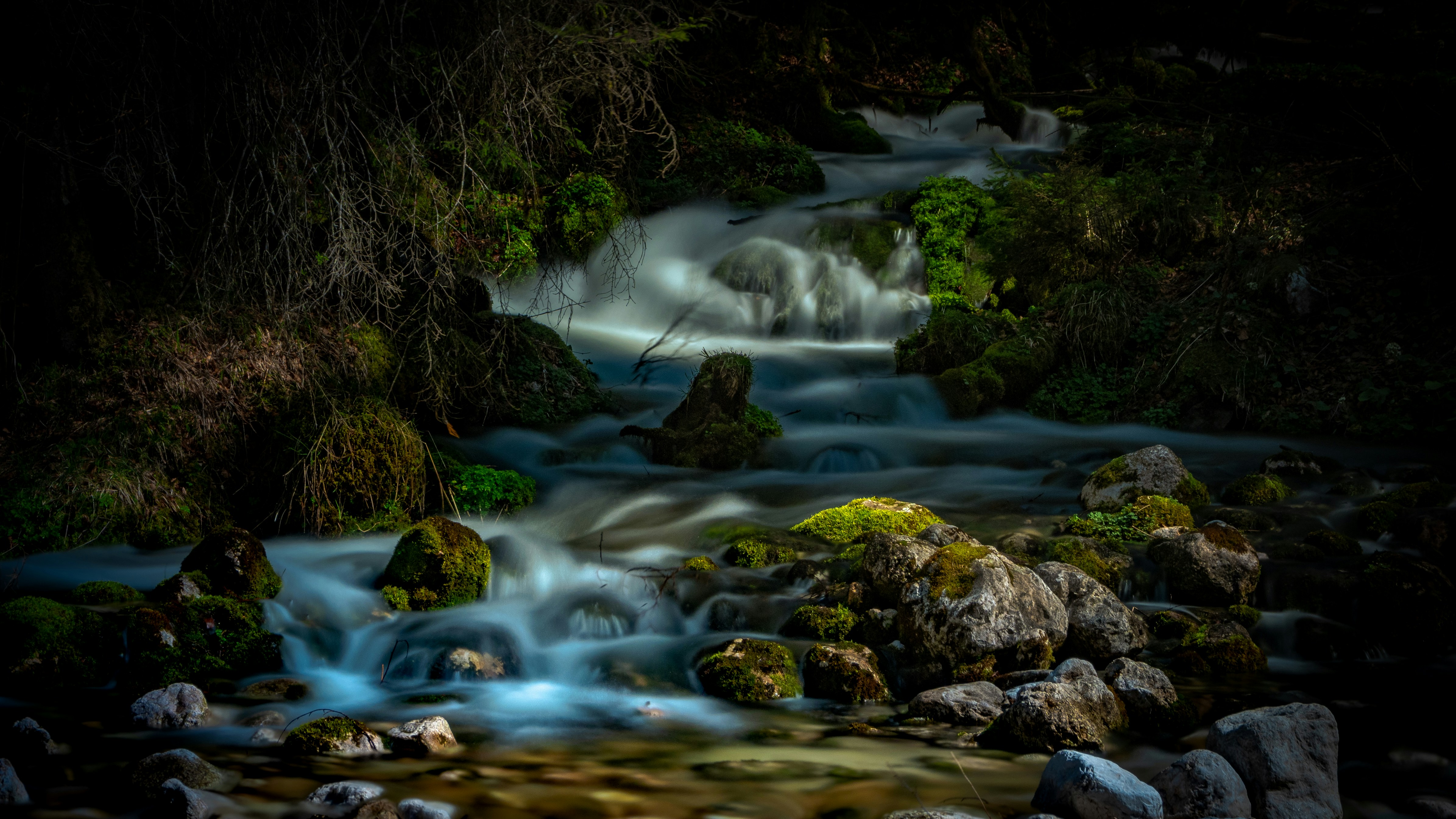 Silky water flows over moss-covered rocks in a shaded forest stream.