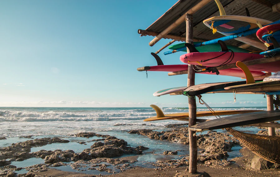 Colorful surfboards stacked on a wooden rack by a rocky shore under a clear blue sky.