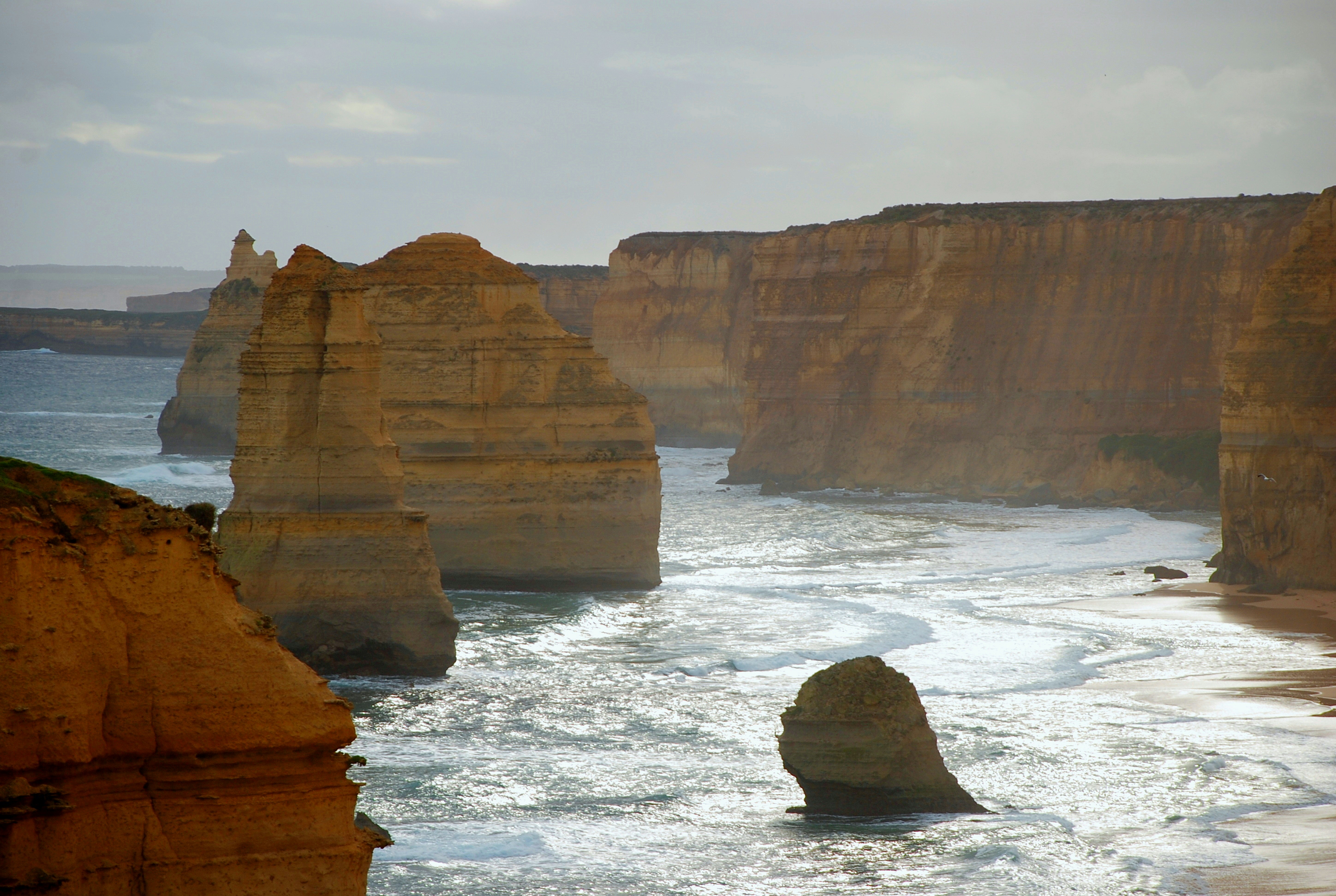 Majestic rock formations rise from the ocean, framed by rugged cliffs and gentle waves. The interplay of light and shadow highlights the natural beauty of this coastal landscape.