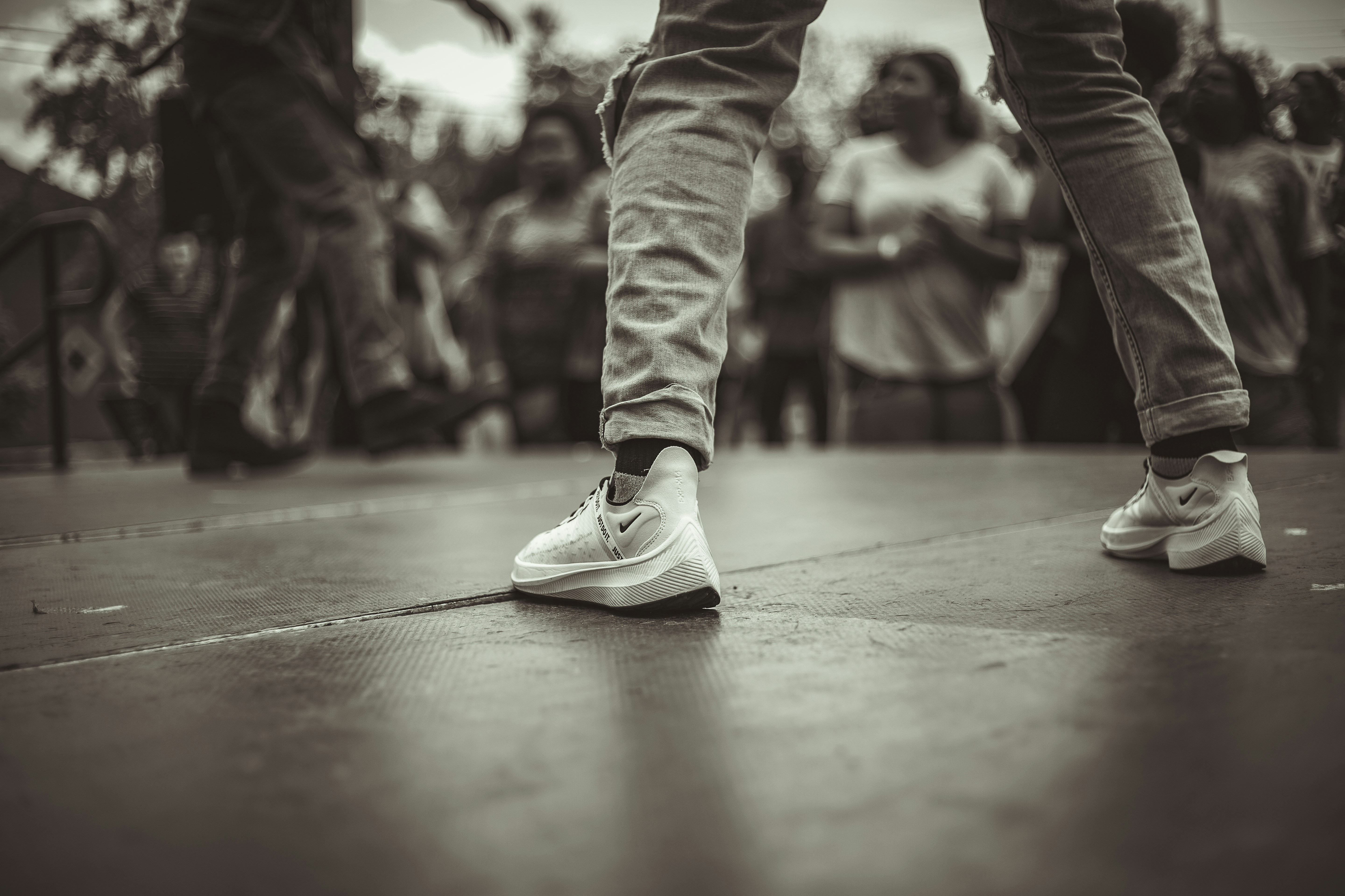 Close-up of a dancer's feet in white sneakers, showcasing movement on a lively dance floor surrounded by an engaged audience.