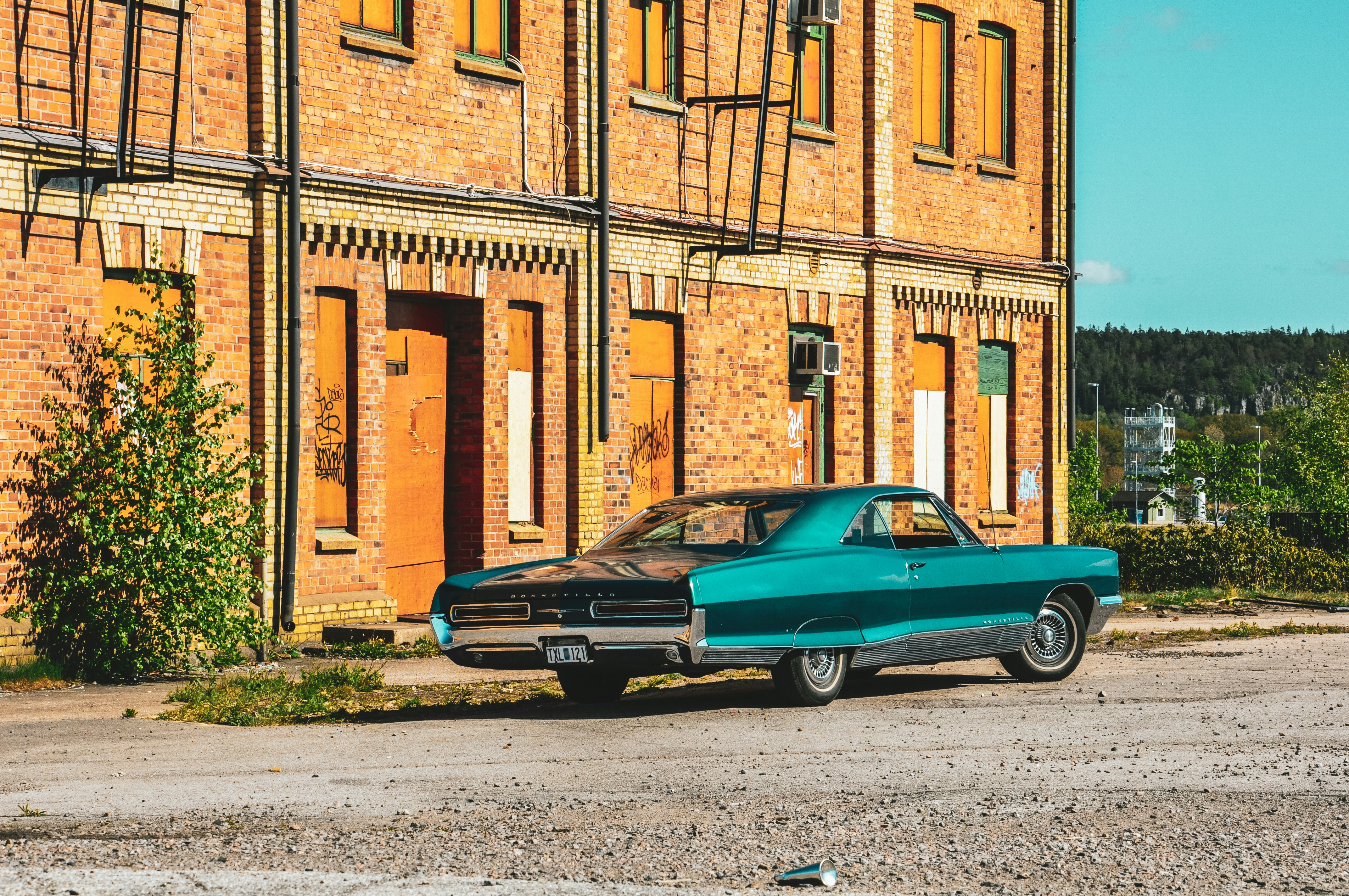 Classic teal car parked near an old brick building under a clear blue sky.