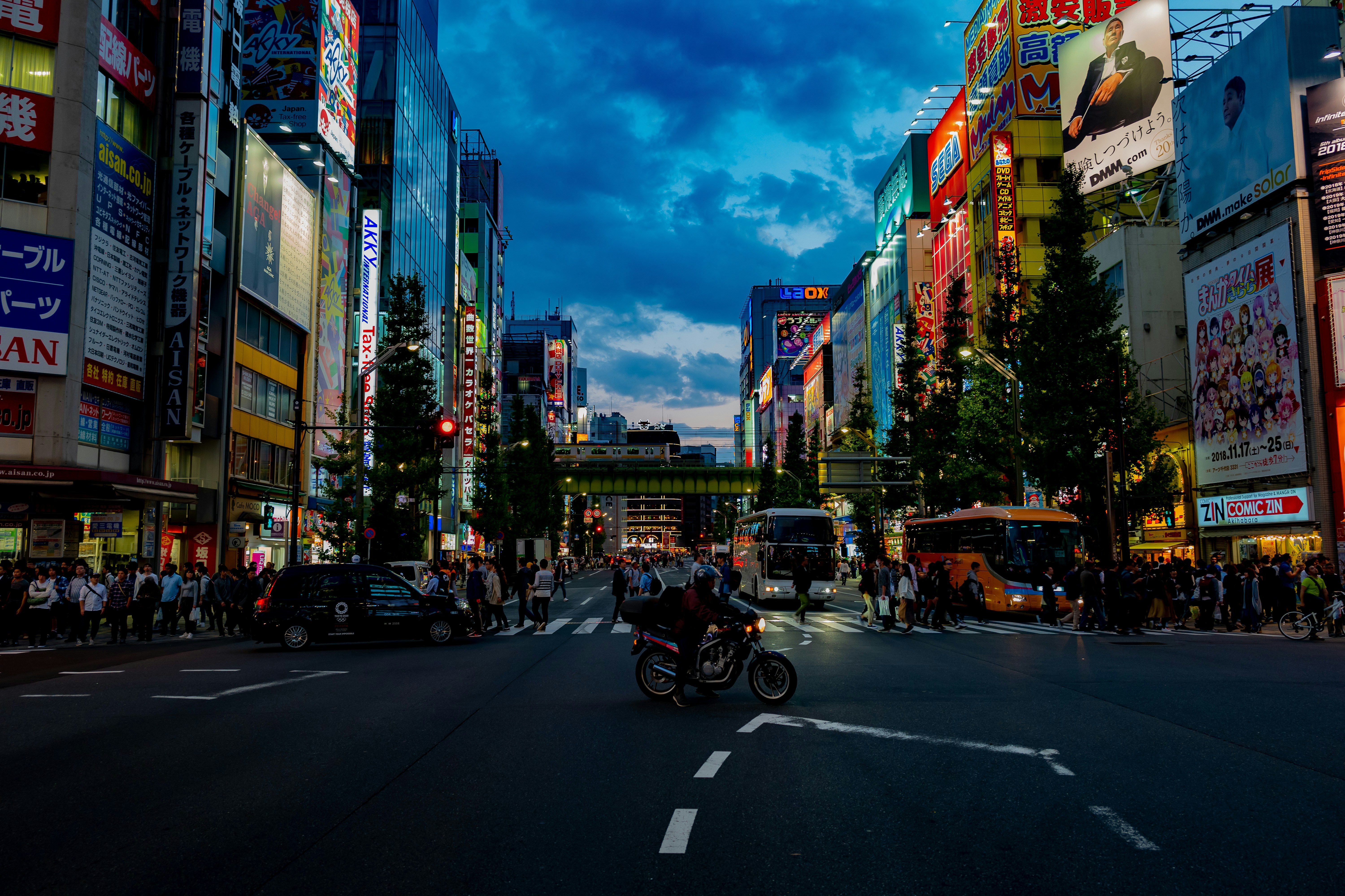 Busy intersection in a vibrant cityscape, illuminated by colorful neon signs and bustling with pedestrians and vehicles.
