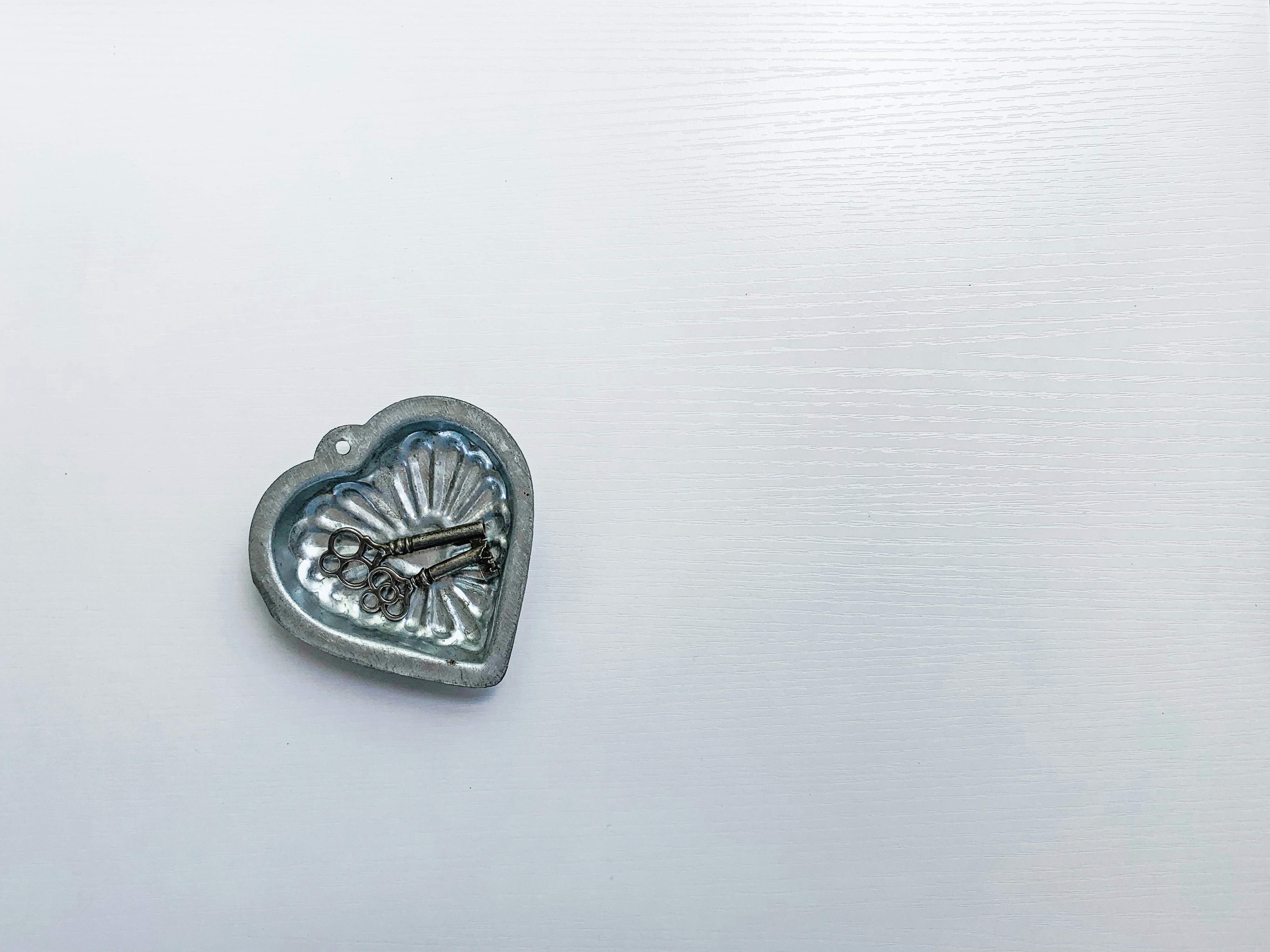 Vintage heart-shaped mold resting on a smooth white surface, showcasing intricate floral designs inside.