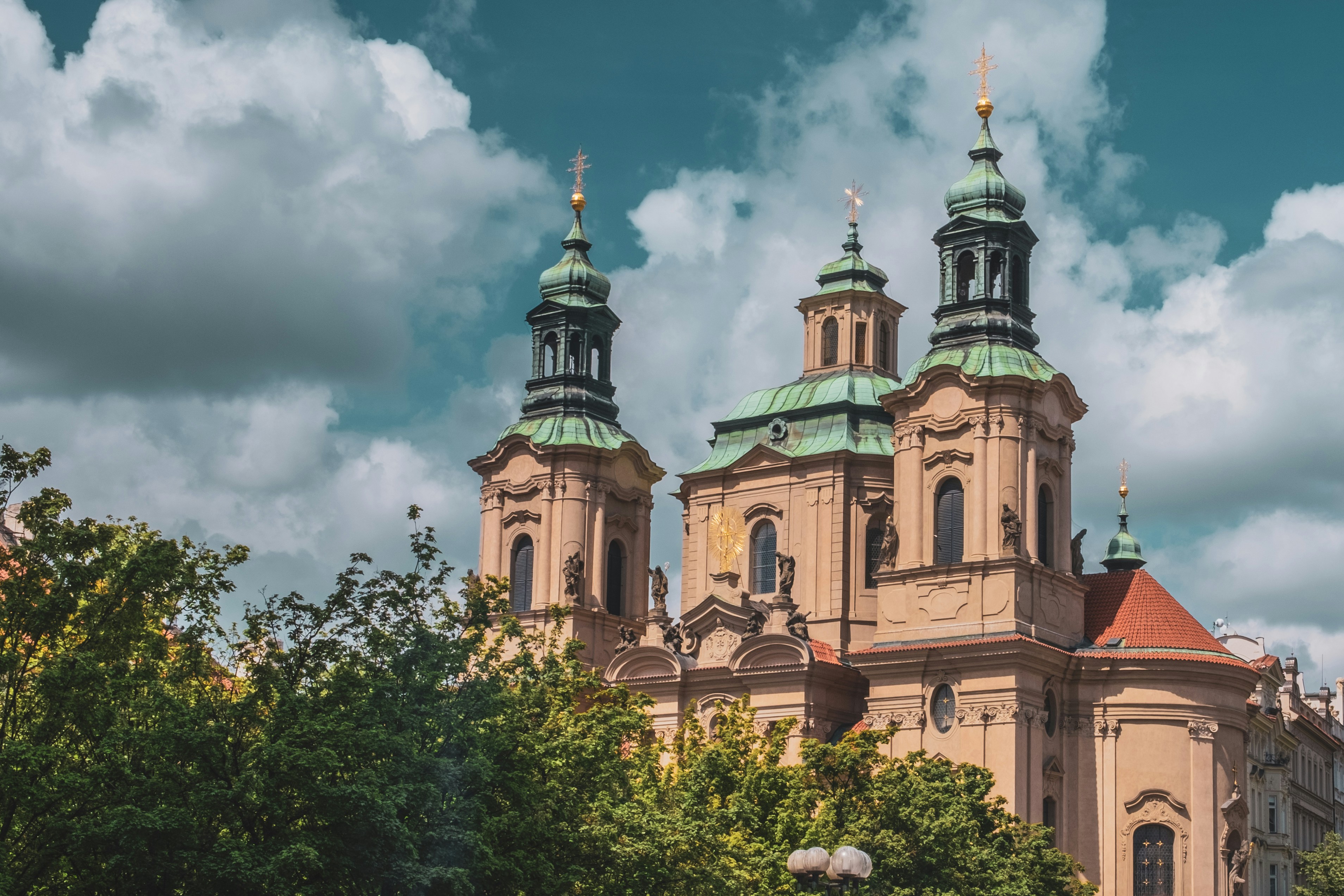 Historic cathedral with teal domes and ornate spires under a cloudy sky.
