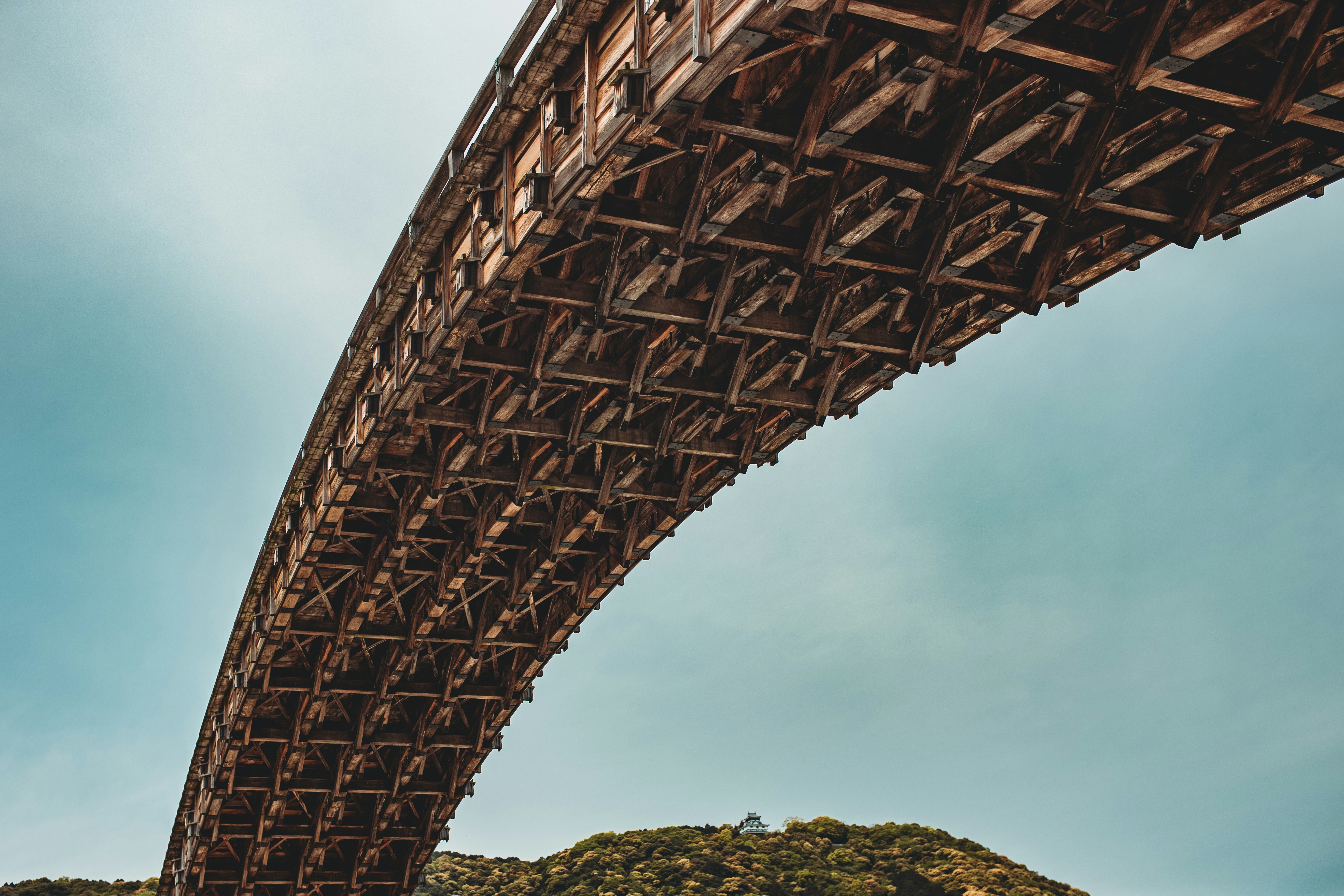 Under the Timbered Curve: A Close View of a Wooden Arch Bridge Against Sky