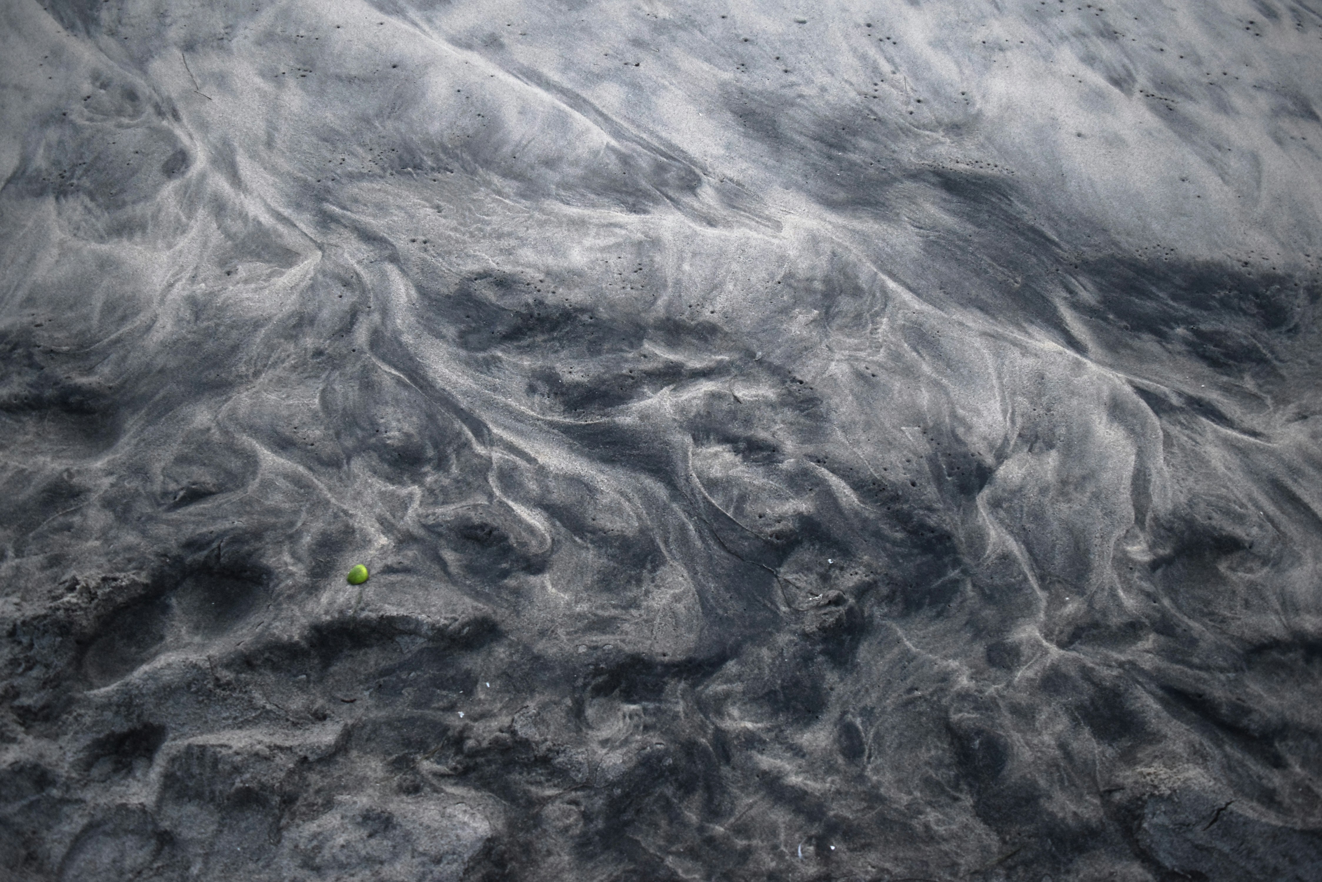 Green tennis ball resting on textured gray sand with swirling patterns.