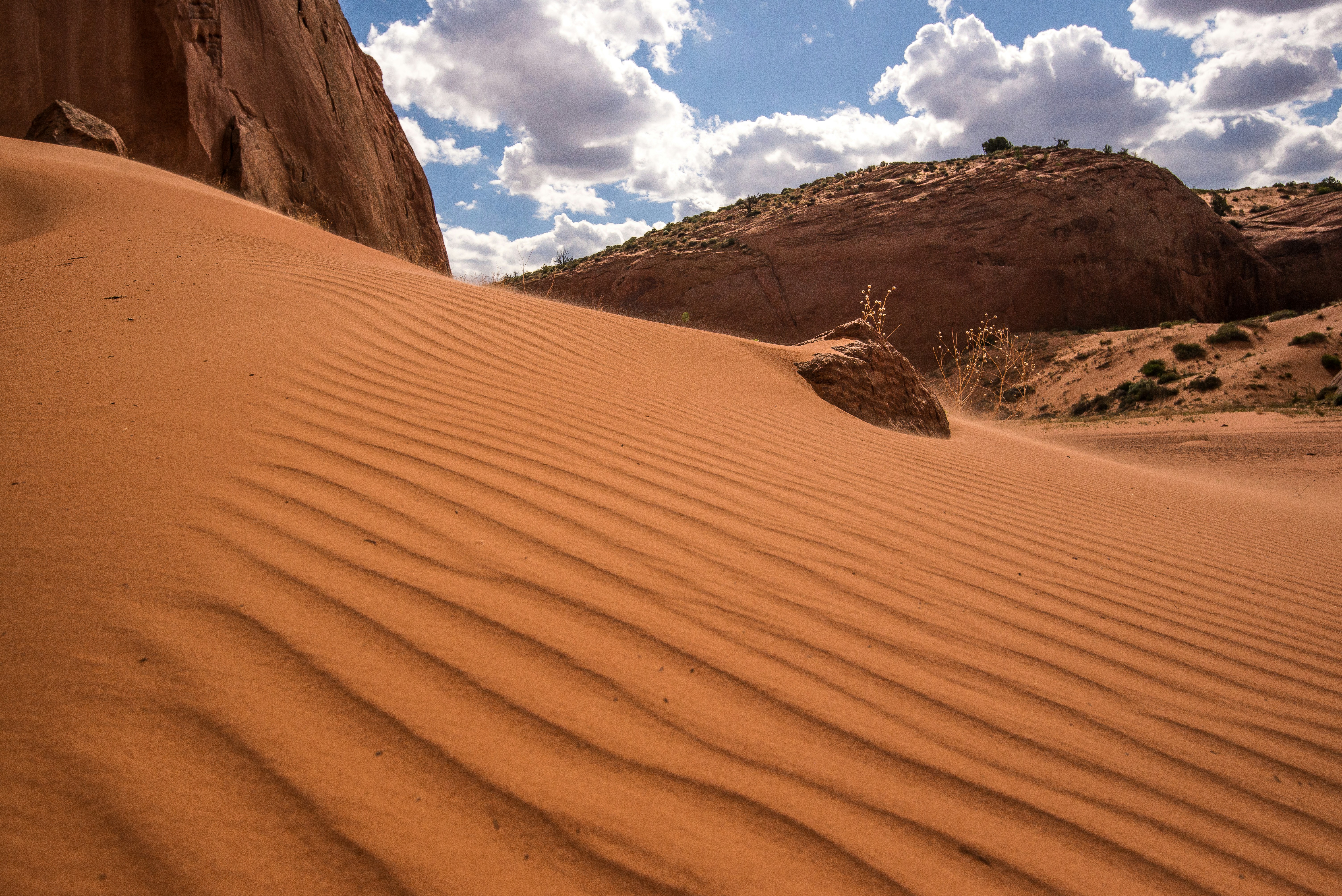Rippling sand dunes under a dynamic sky, showcasing the interplay of light and shadow in a desert landscape.