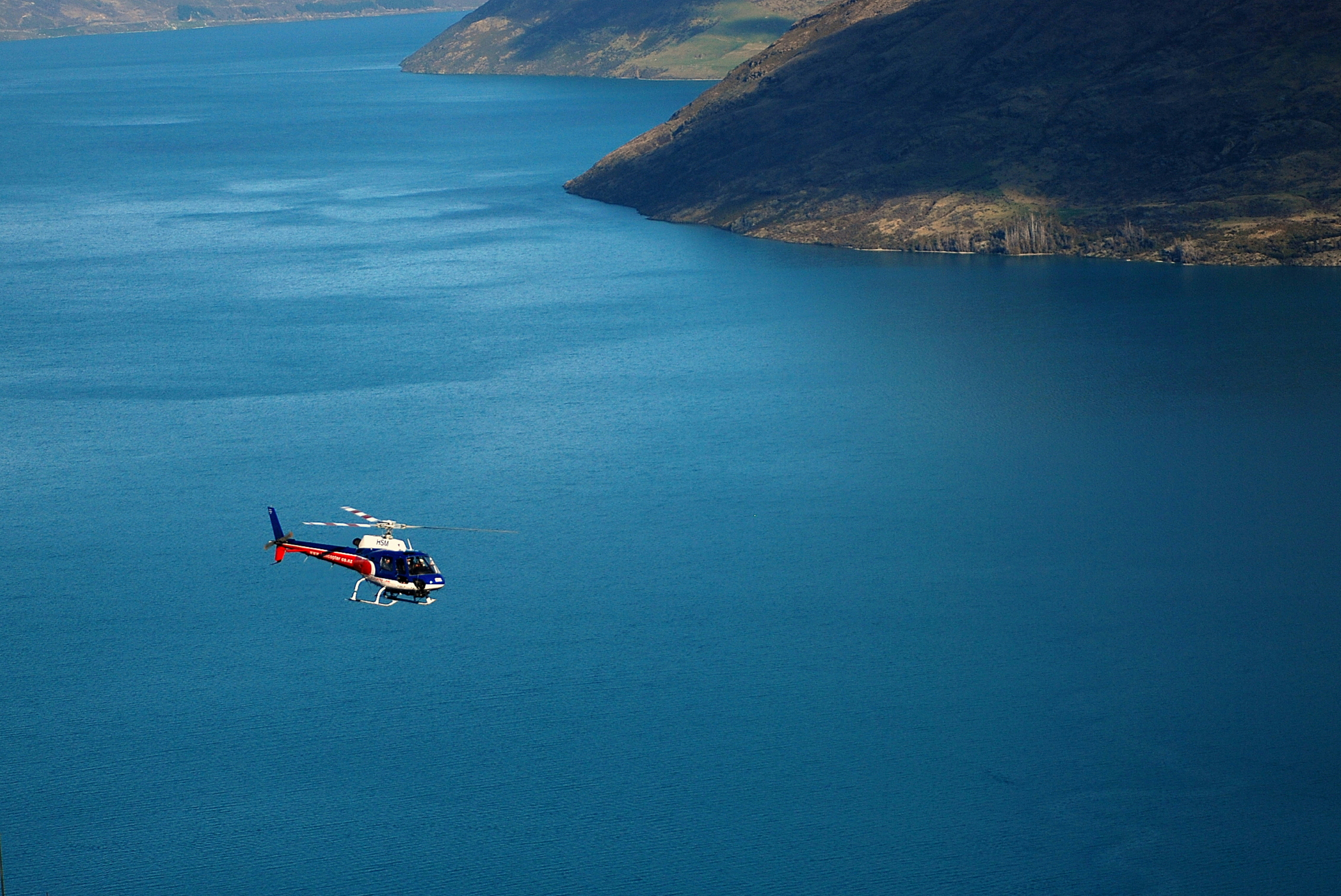 Azure Expanse: A Red-White Husky Rescue Helijet Drifts Over Fjordly waters