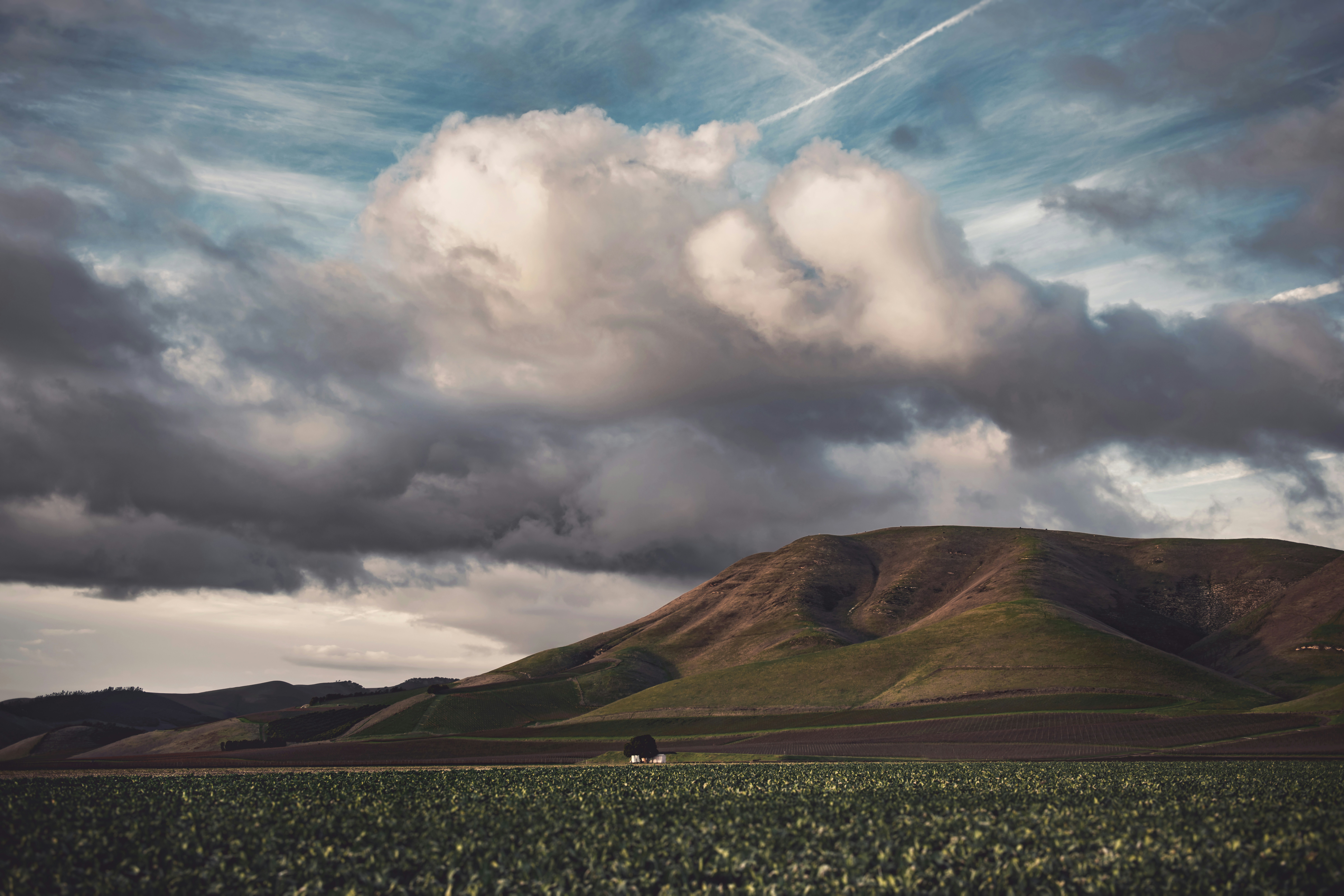 Lone farmhouse nestled in a vast green field beneath a dramatic sky filled with clouds.