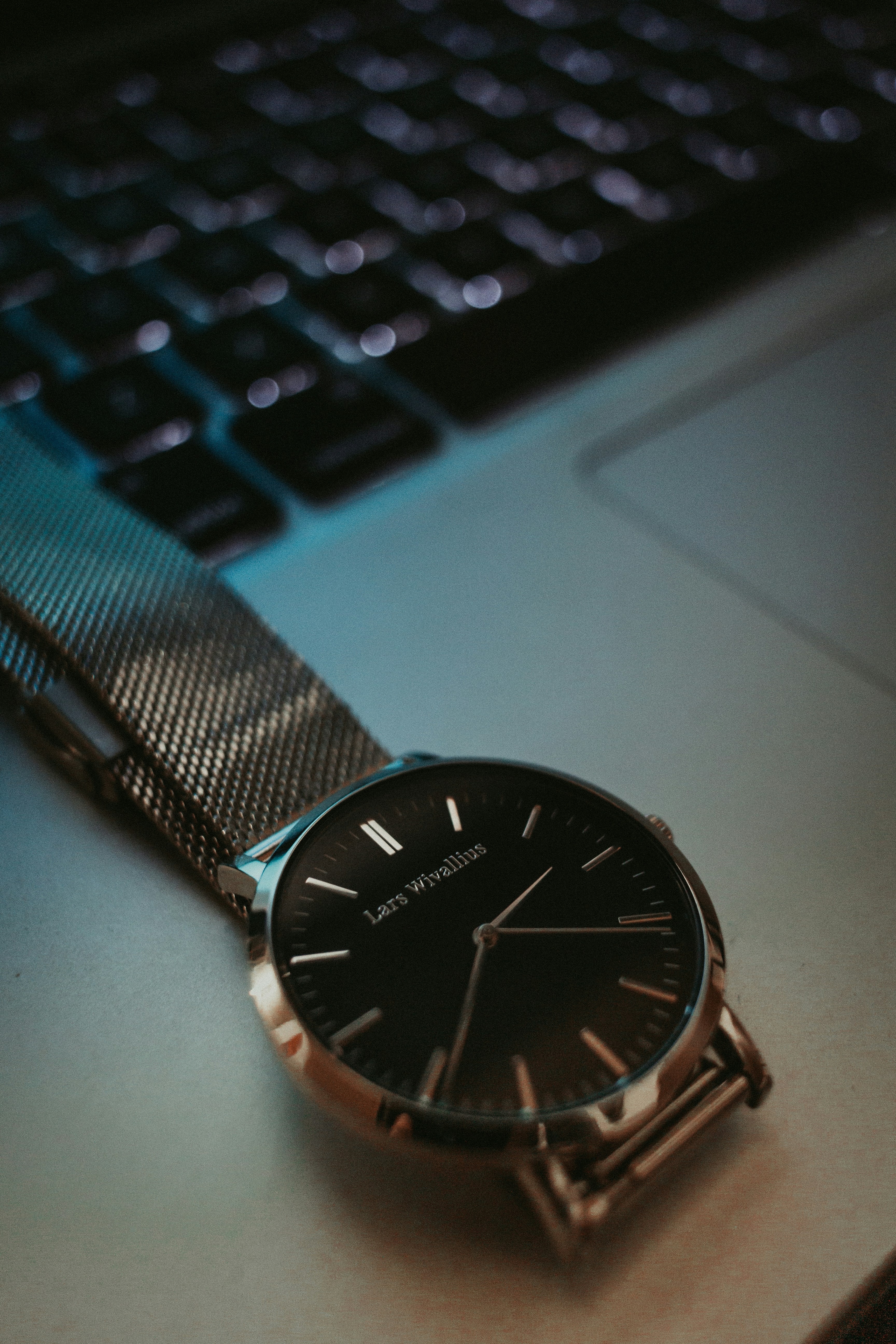 Looming Minute: A steel mesh watch on a cool blue desk with a softly blurred keyboard backdrop