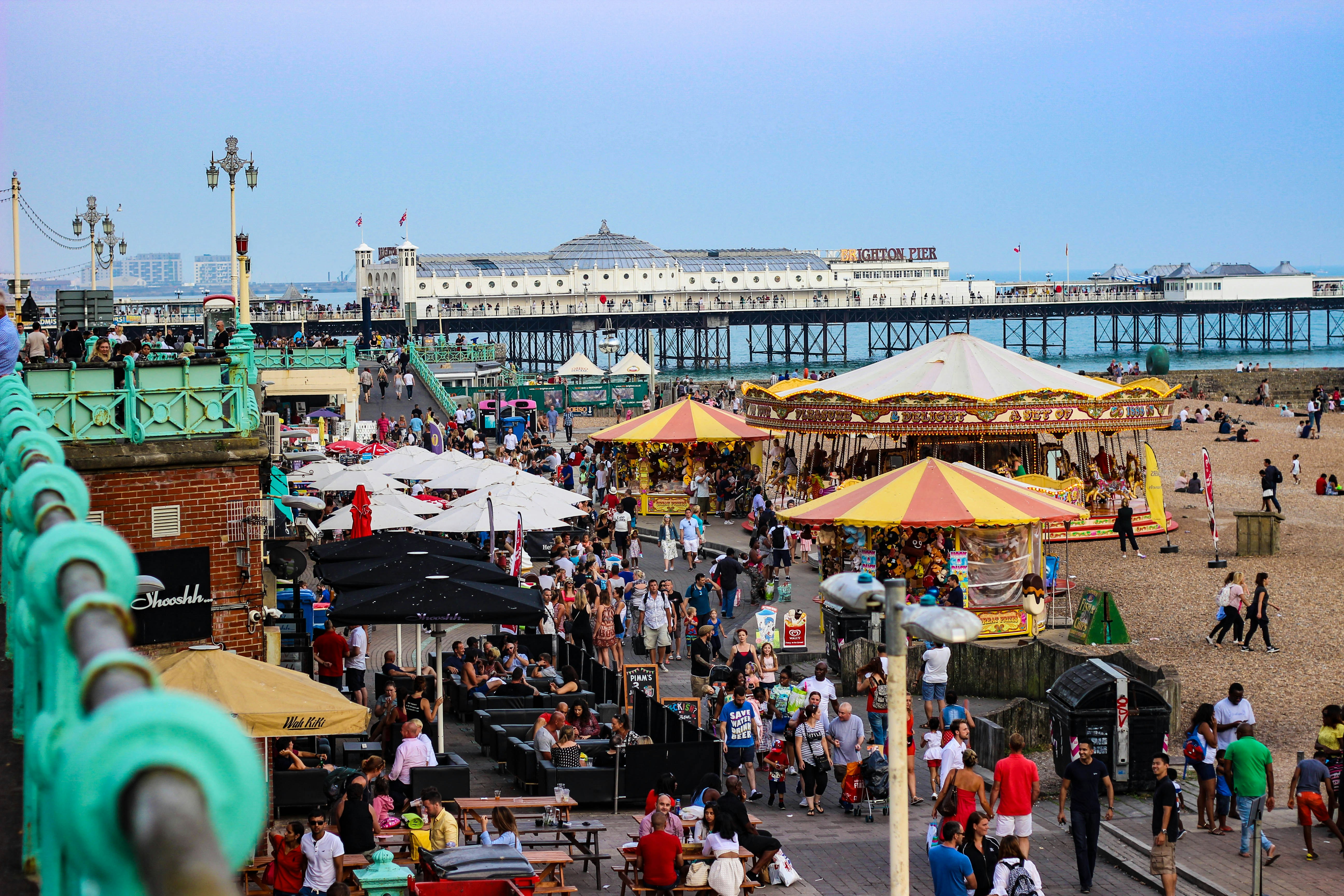 Crowded beach with colorful umbrellas and a pier in the background under a clear sky.
