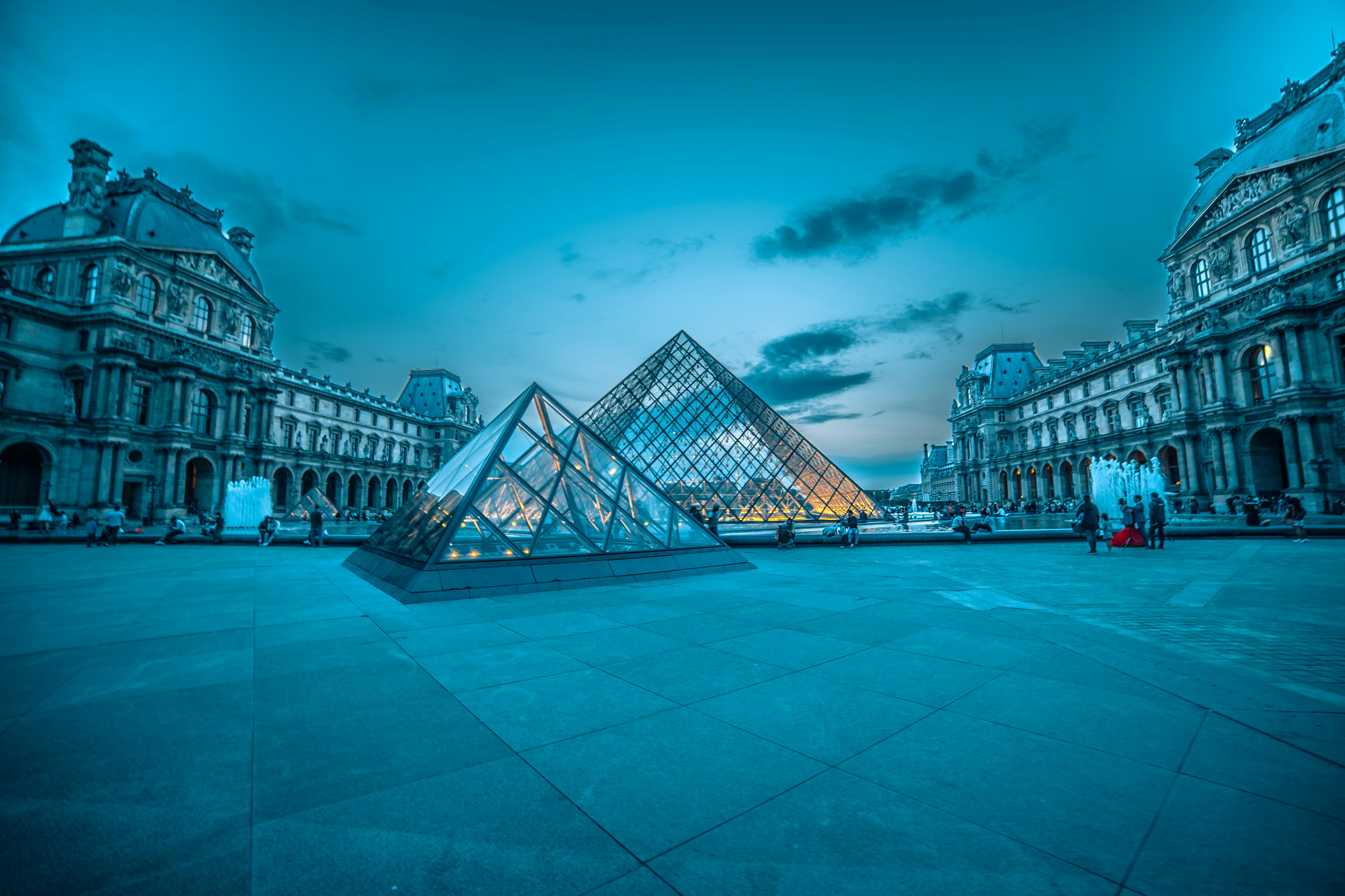 Illuminated glass pyramids contrast against the historic architecture of the Louvre, showcasing a blend of modern and classical design.