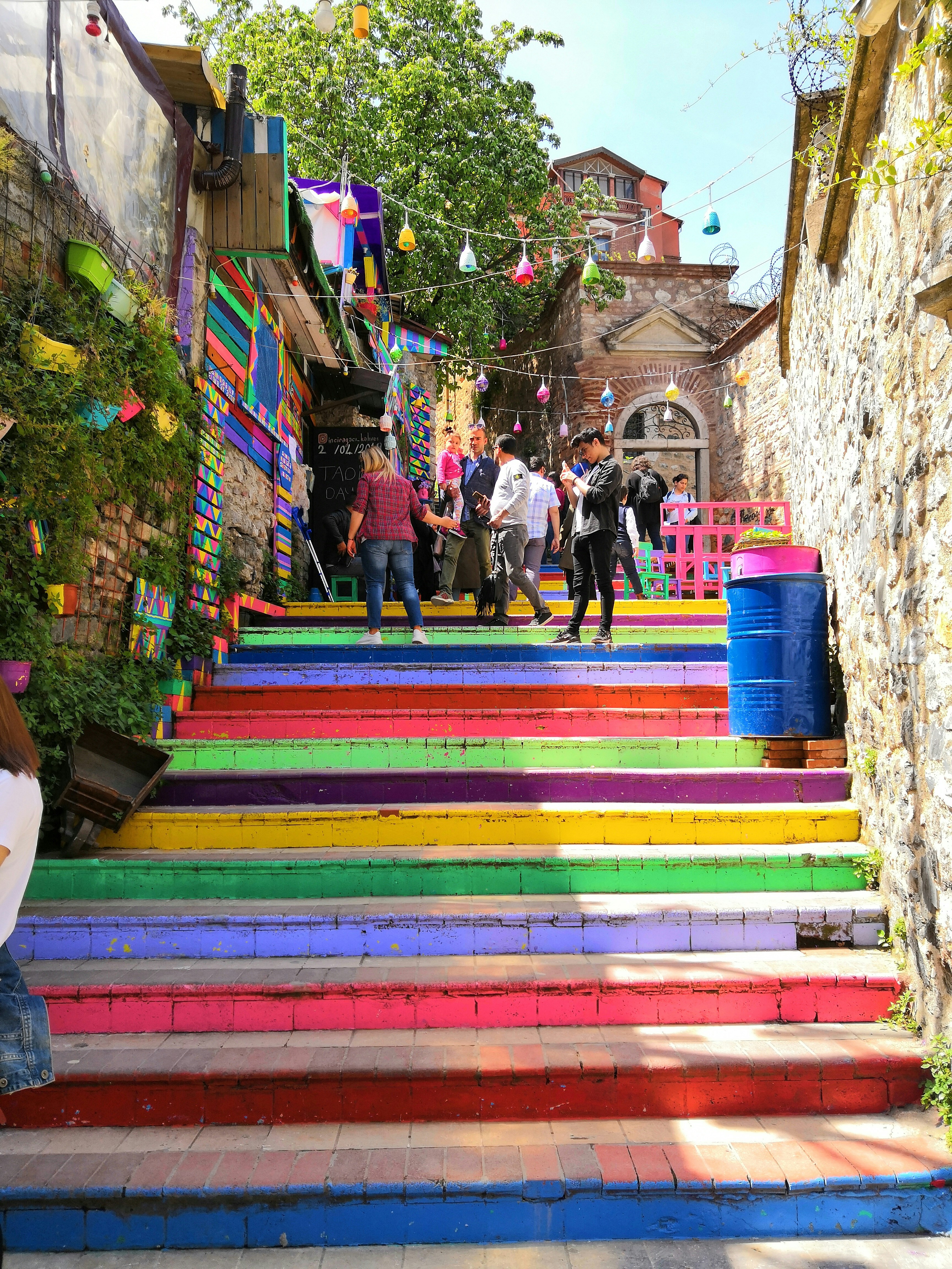 People ascending colorful stairs adorned with lively decorations and hanging lights in a lively urban setting.