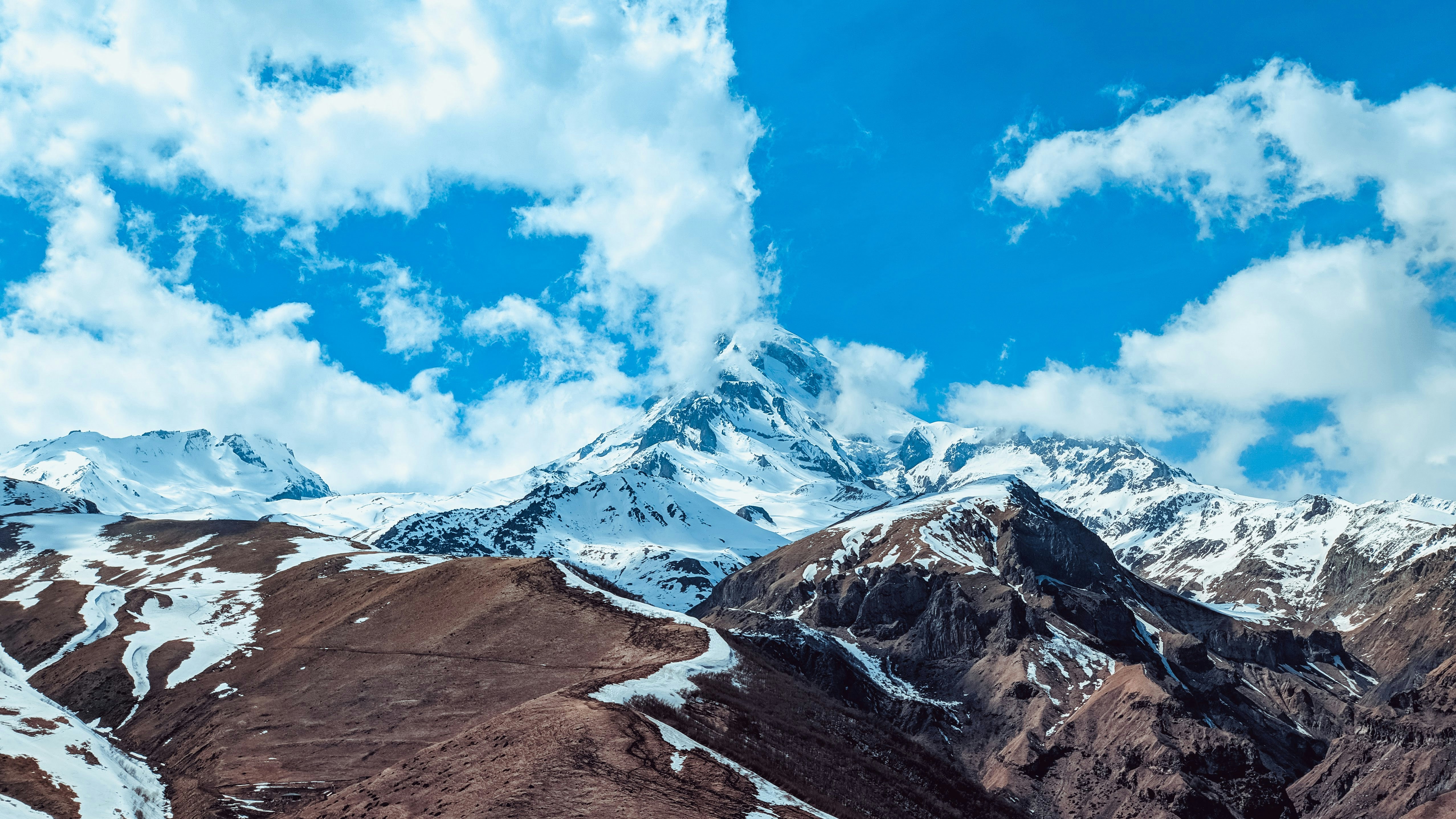 Snow-capped mountains rise beneath a vibrant blue sky dotted with fluffy clouds.
