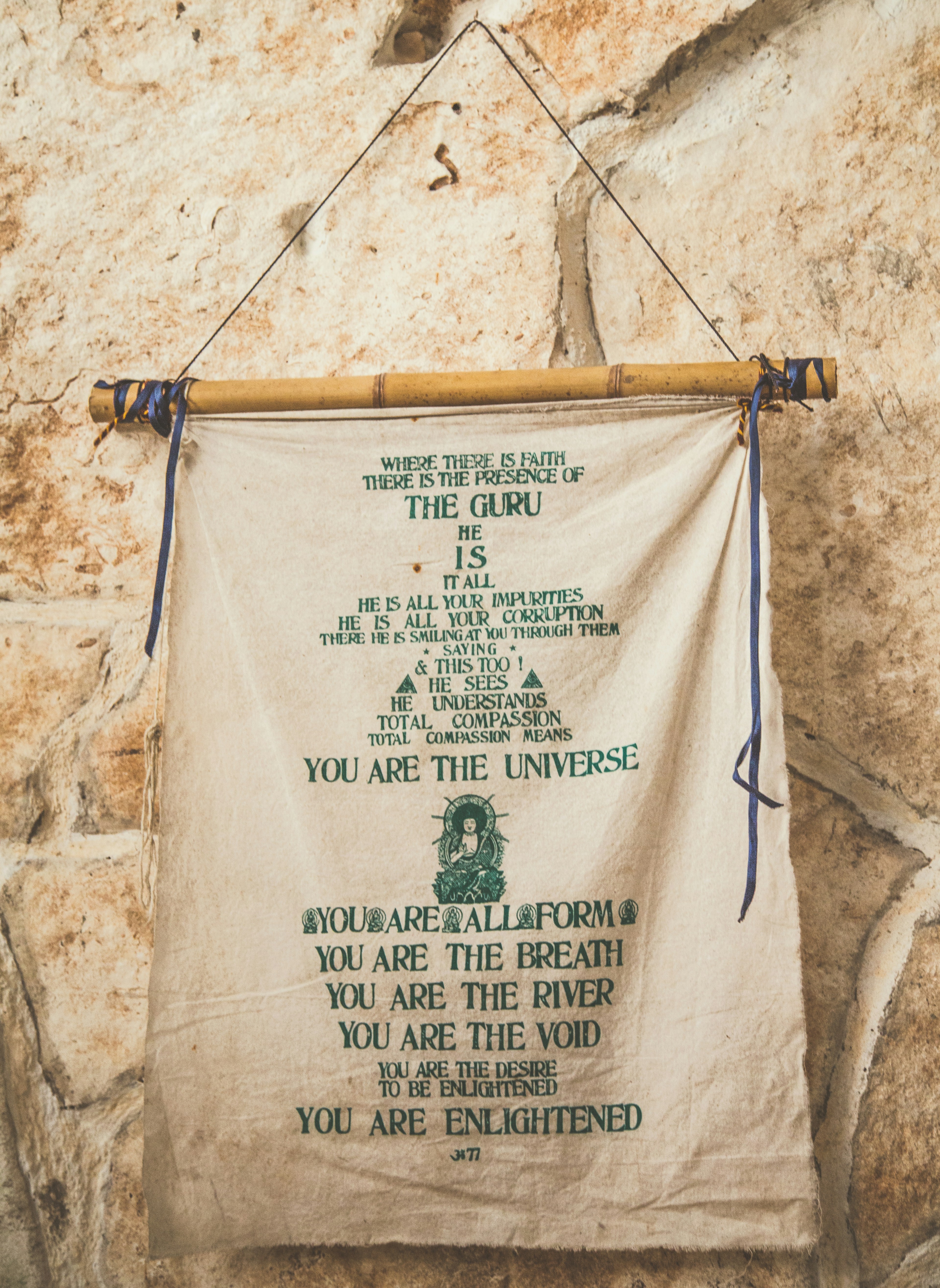 A fabric banner displaying a spiritual message about the essence of the universe and enlightenment, hanging from a bamboo rod against a textured wall.