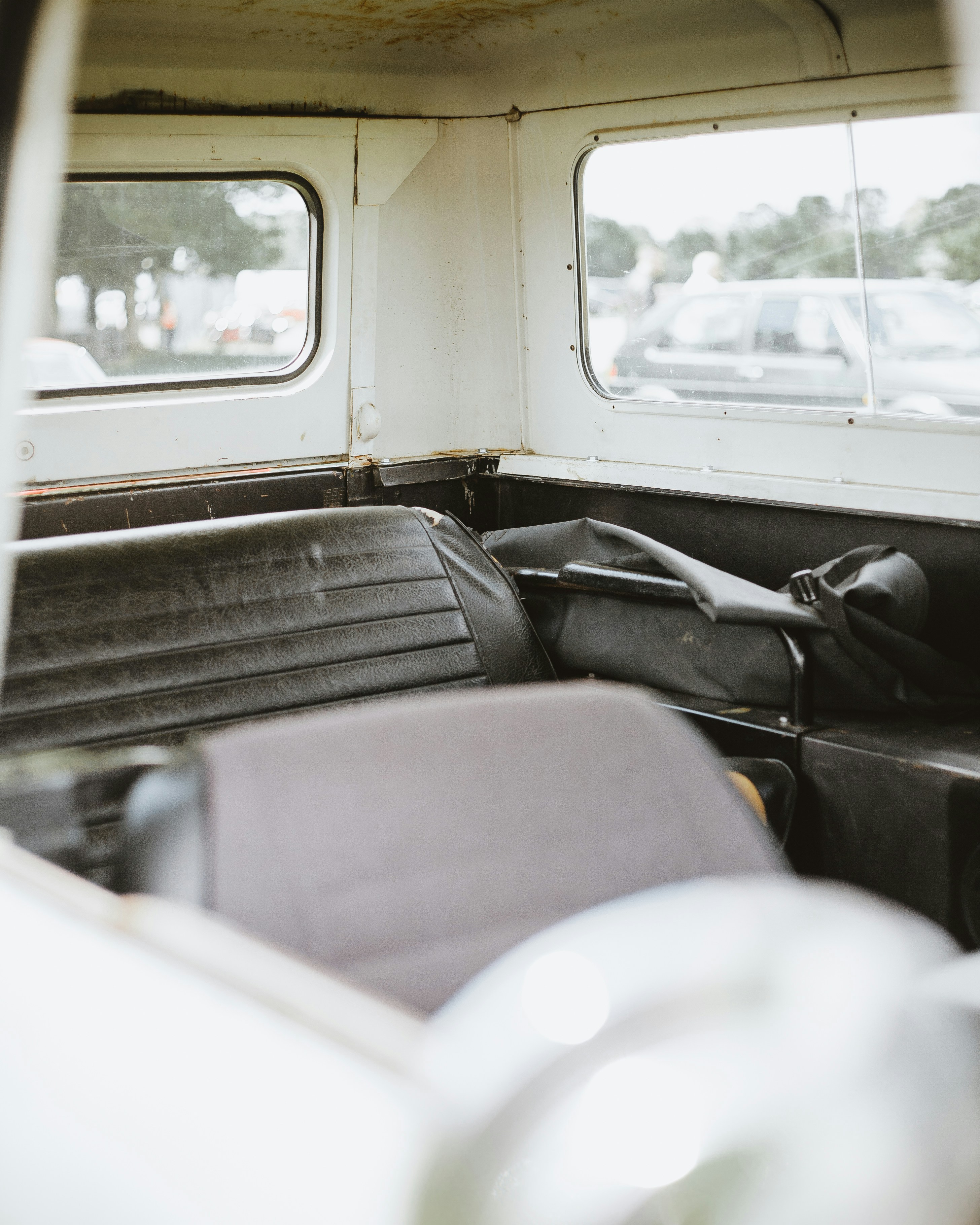 Interior of a vintage vehicle showcasing worn seats and a rustic aesthetic, framed by windows revealing a blurred exterior. 
