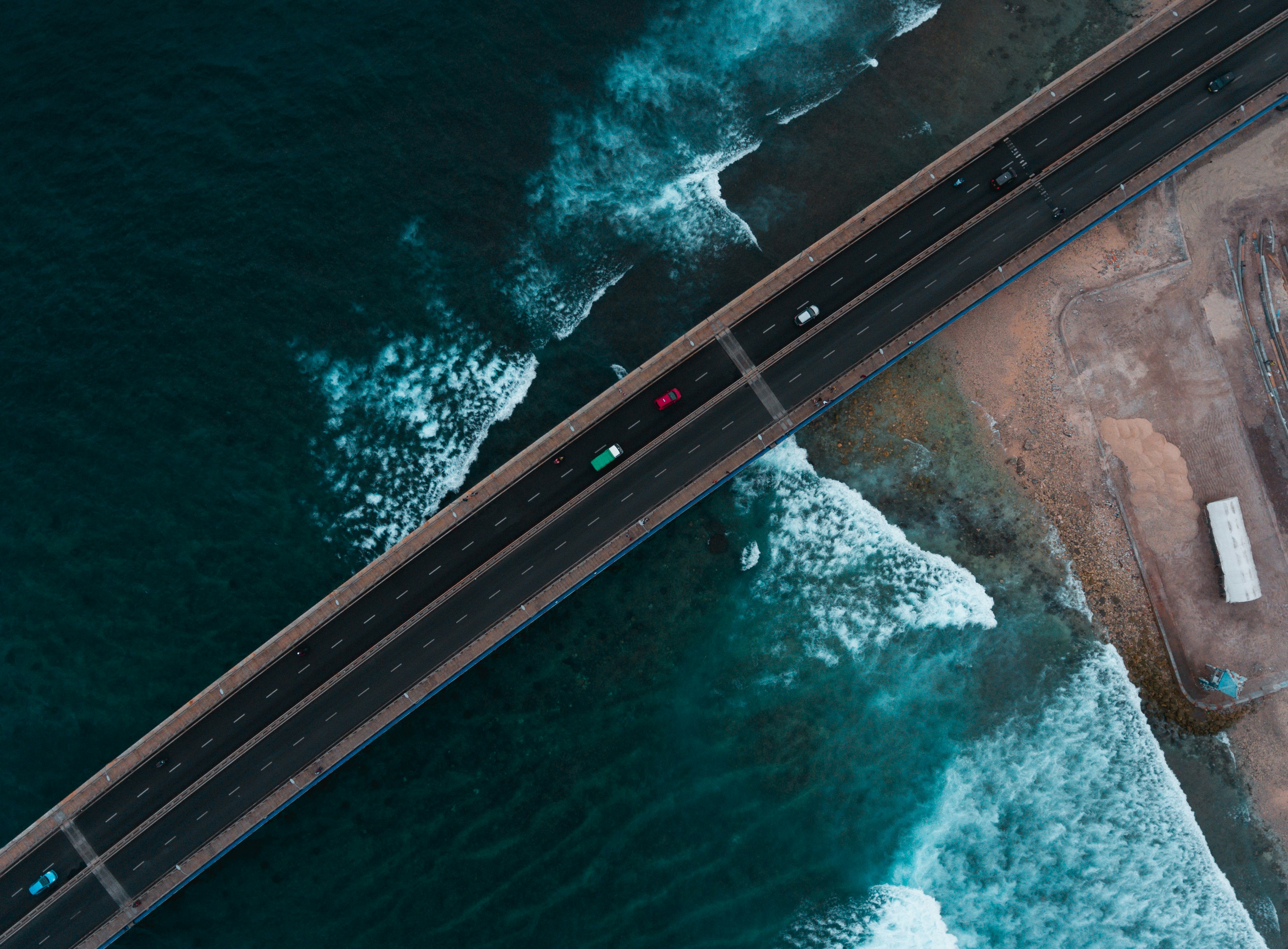 Aerial view of a coastal road intersecting the ocean as waves crash against the shore.