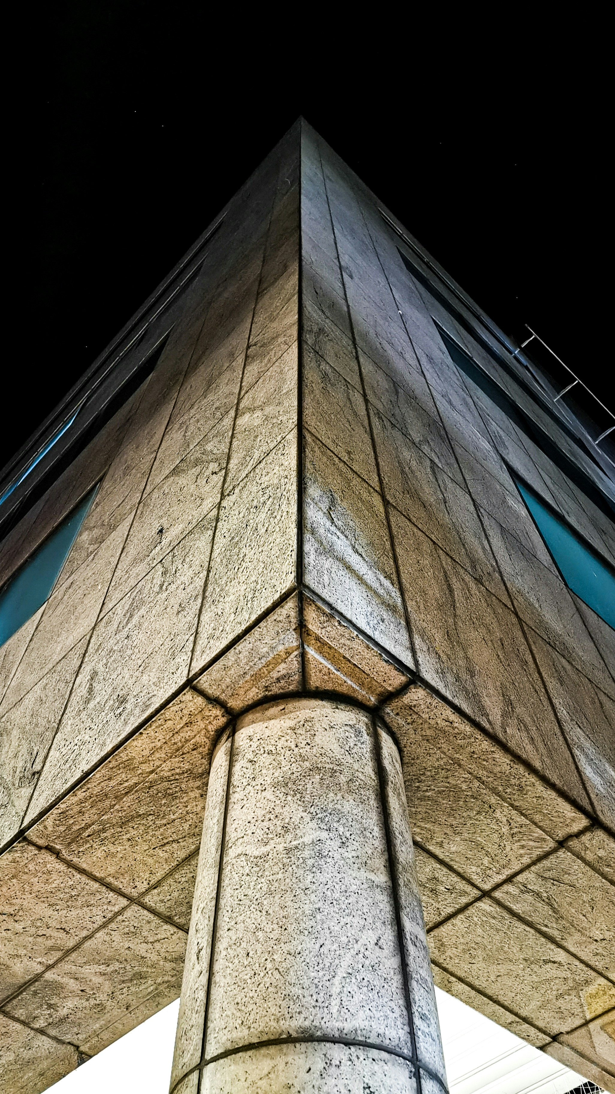 Sharp corner of a modern building captured from below, emphasizing its geometric lines and textures against a dark sky.