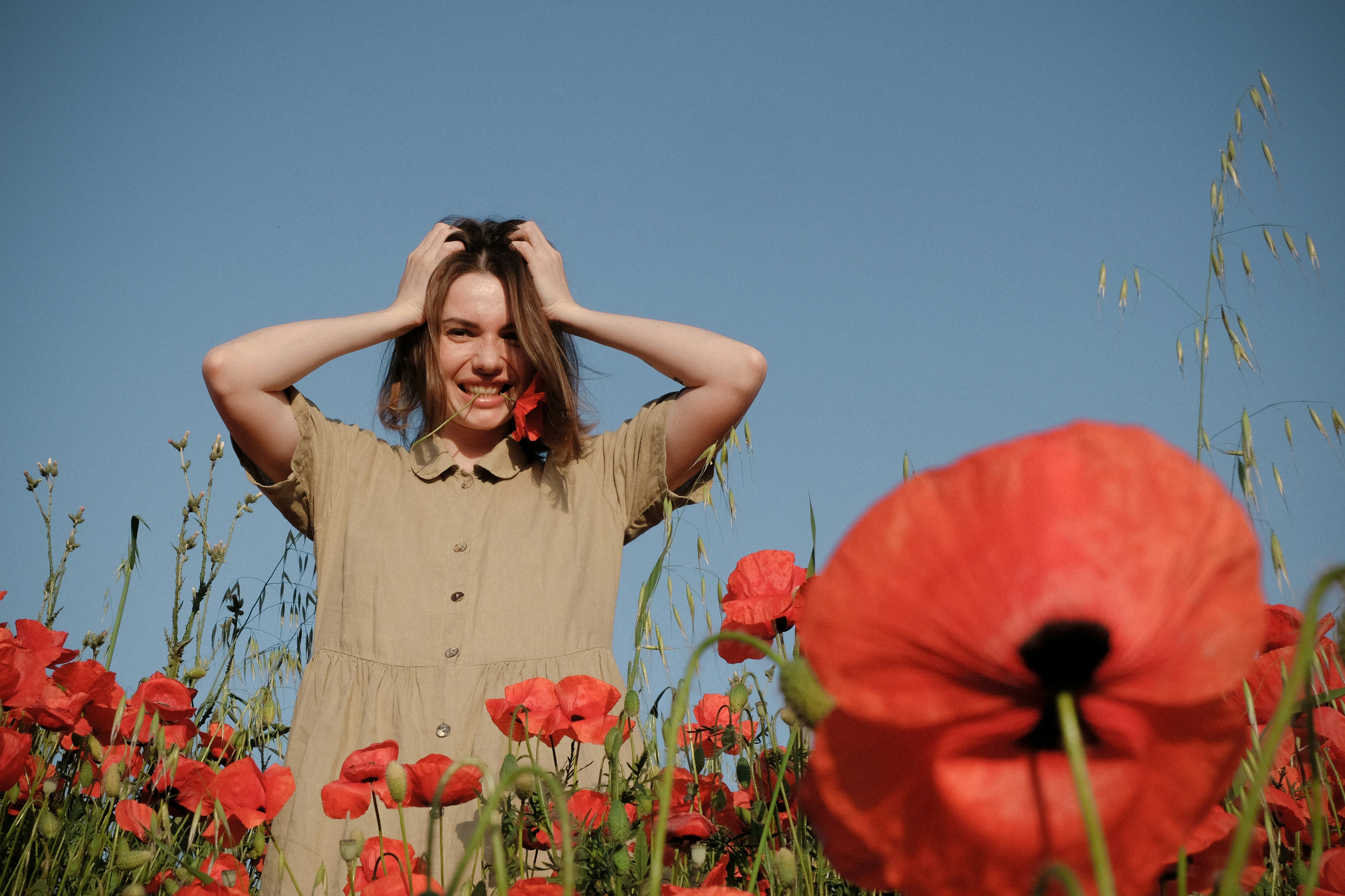 Woman with a joyful expression surrounded by vibrant red poppies in a sunny field.