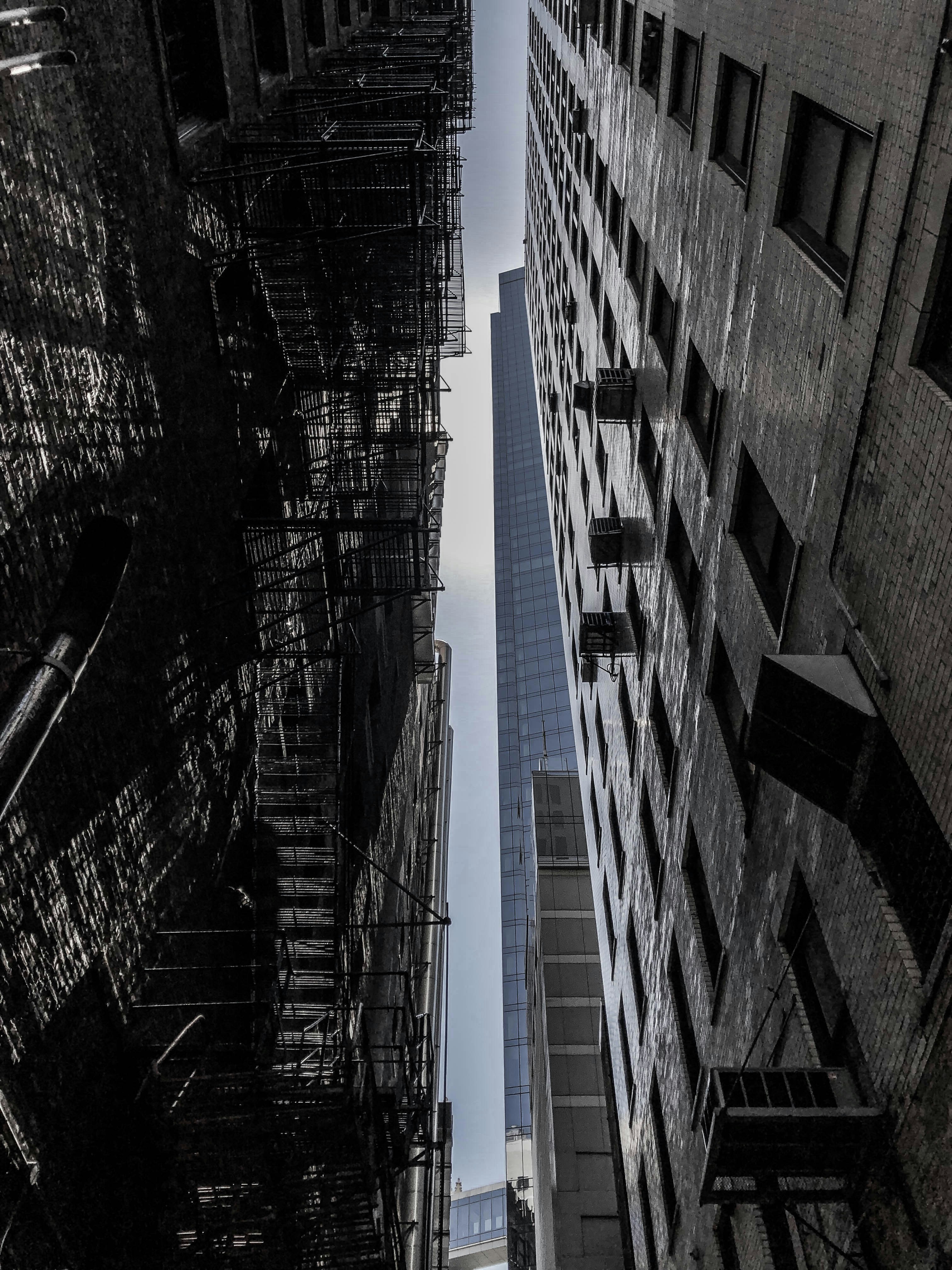 Tall buildings and fire escapes create a dramatic urban canyon view under a cloudy sky.