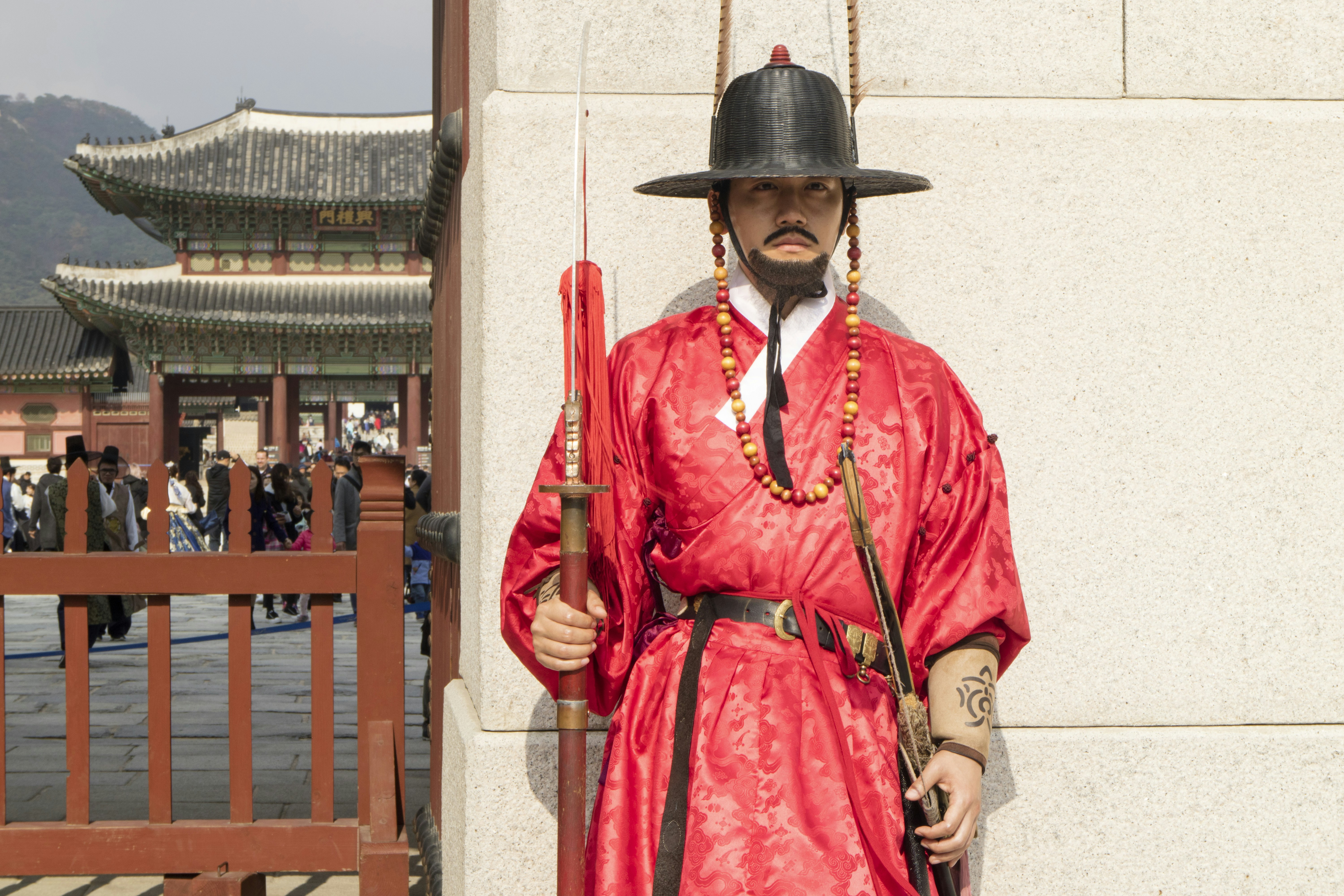 A traditional Korean guard in vibrant red attire stands at attention near a historic palace entrance, showcasing cultural heritage.