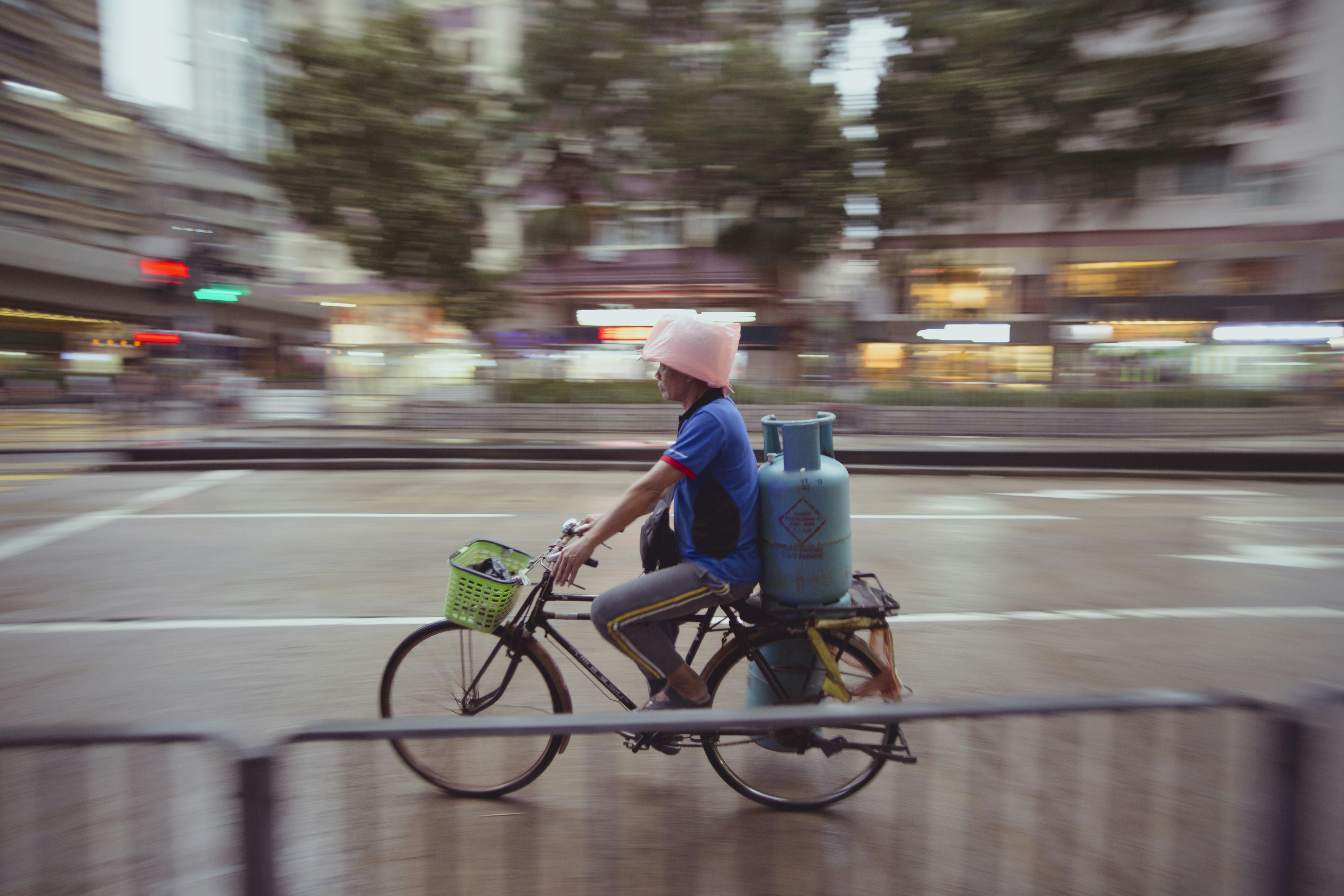Cyclist navigating a bustling city street while transporting a gas cylinder, captured in motion blur to emphasize speed and activity.