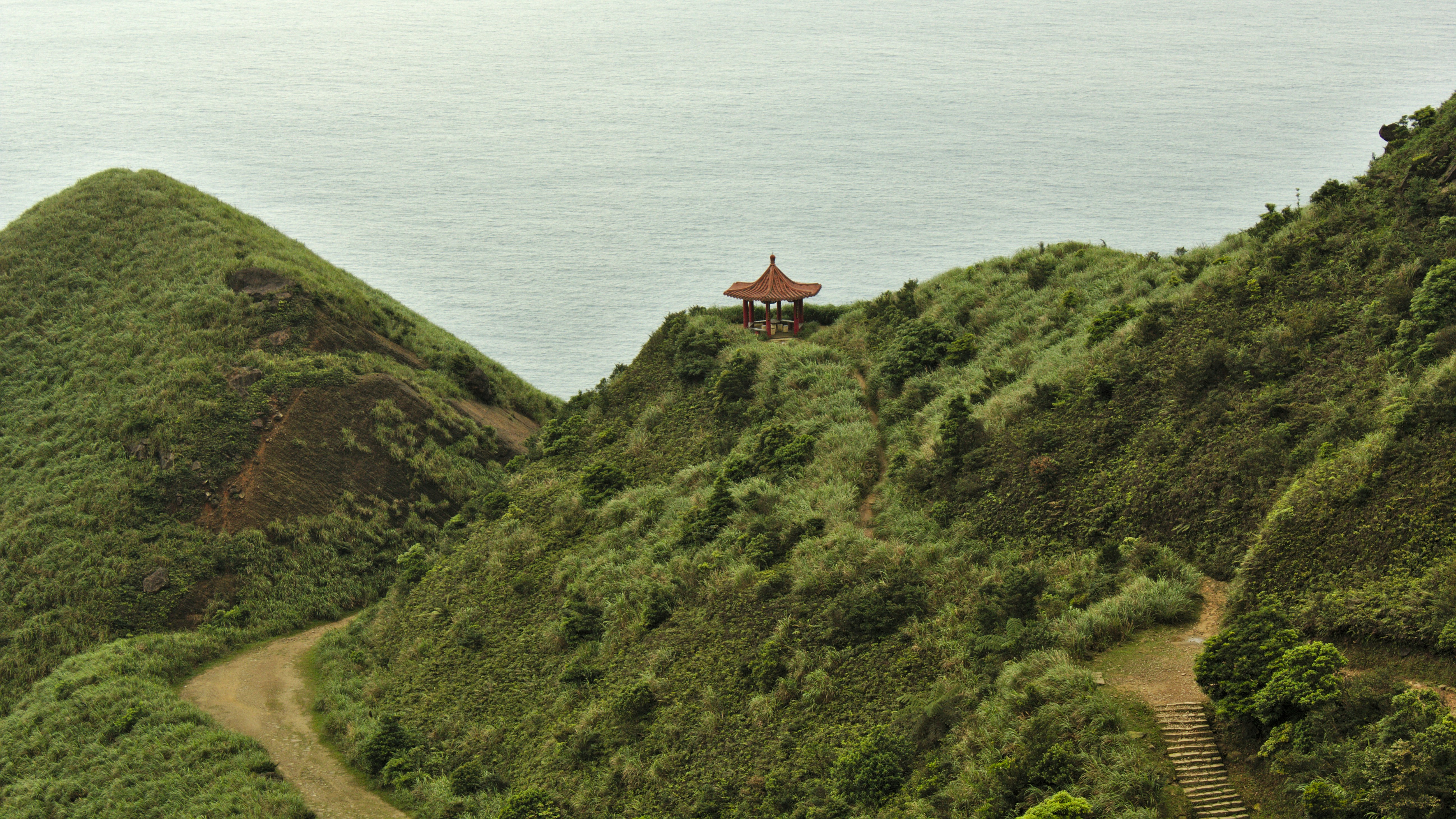 Traditional gazebo perched on a hillside overlooking the ocean, surrounded by lush greenery. A tranquil escape in nature.