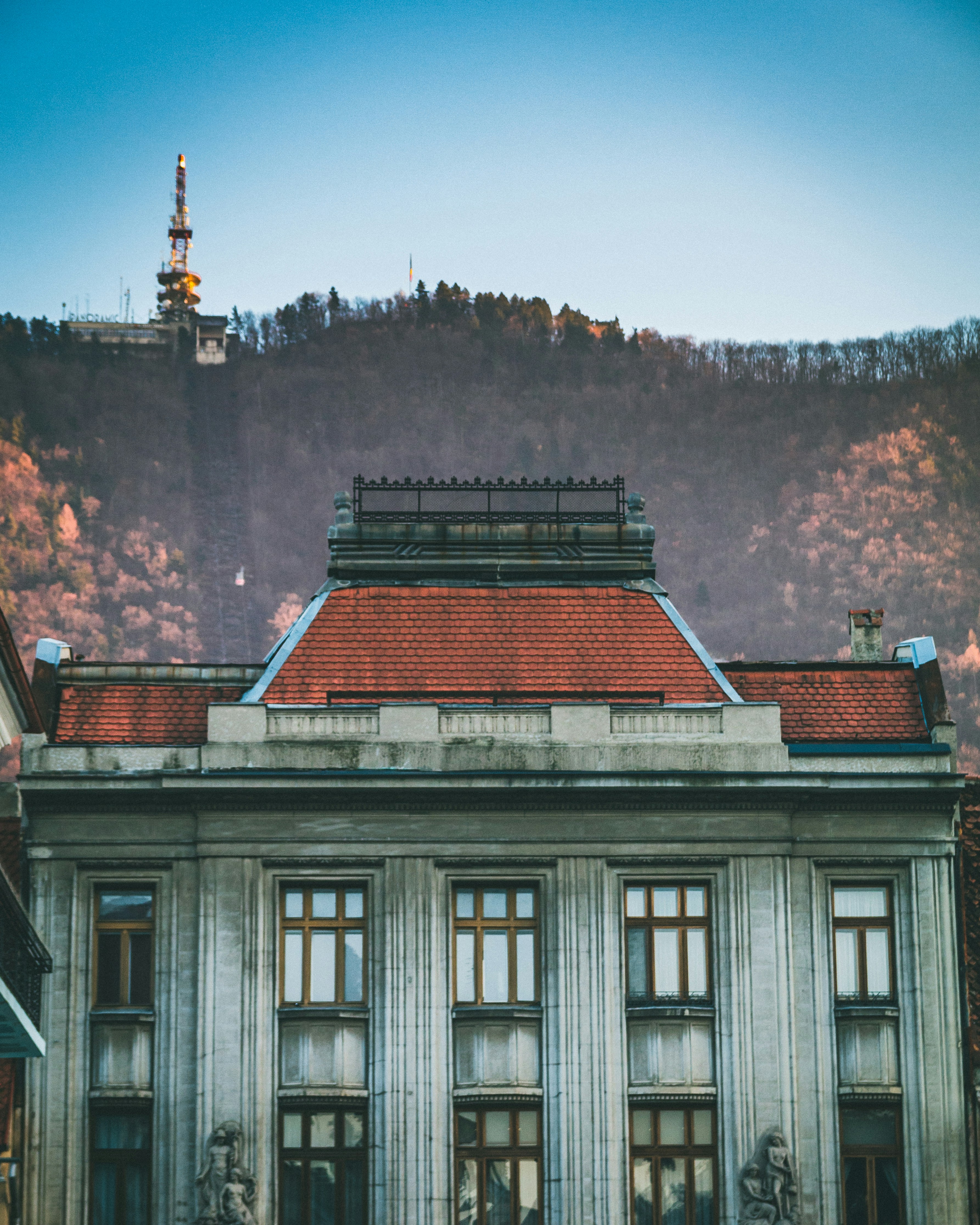 Historic building with intricate architectural details set against a backdrop of a mountainous landscape and communication tower.