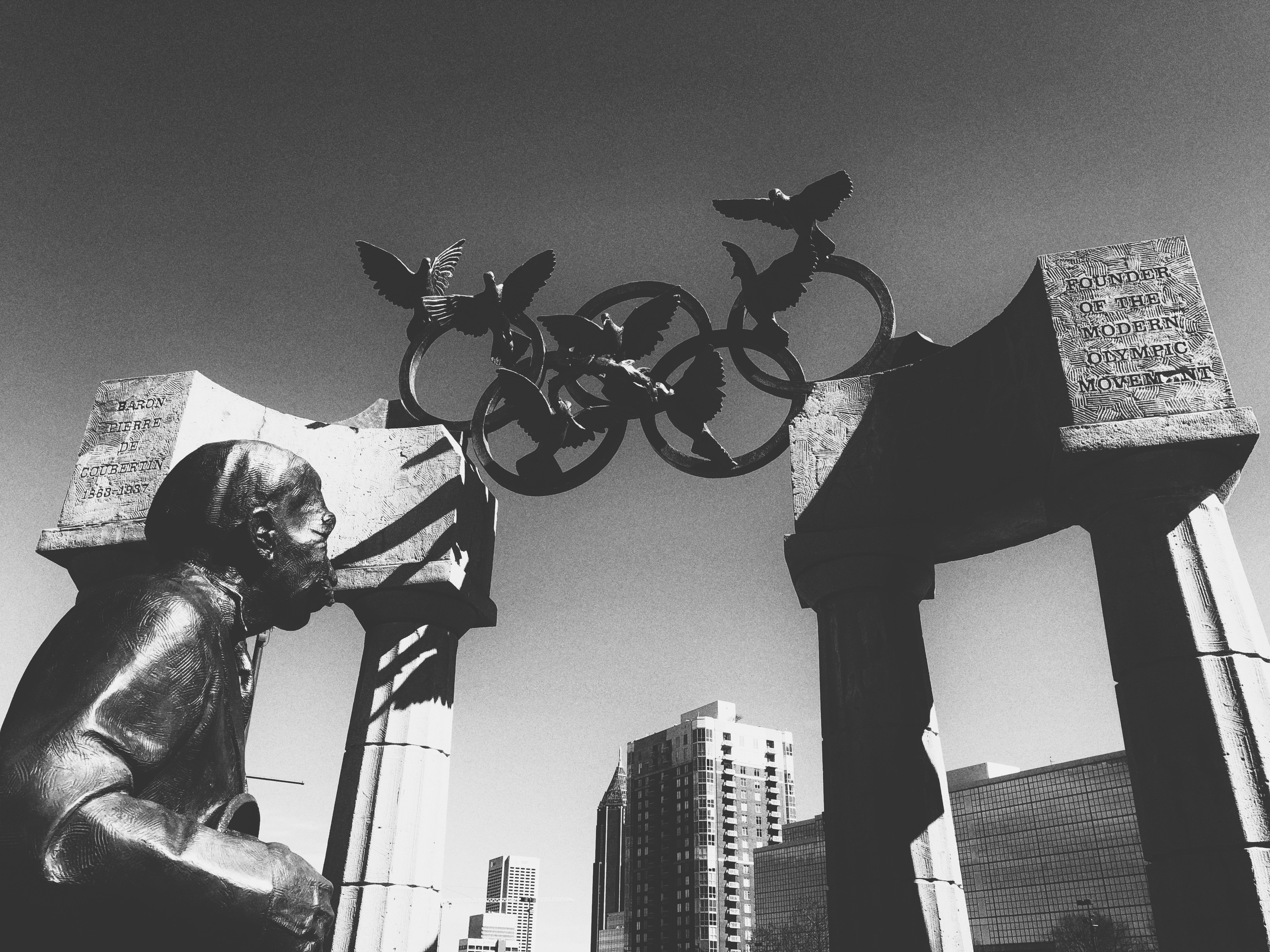 A bronze statue gazes upward at a striking arch adorned with birds and inscriptions, symbolizing the spirit of modern governance.