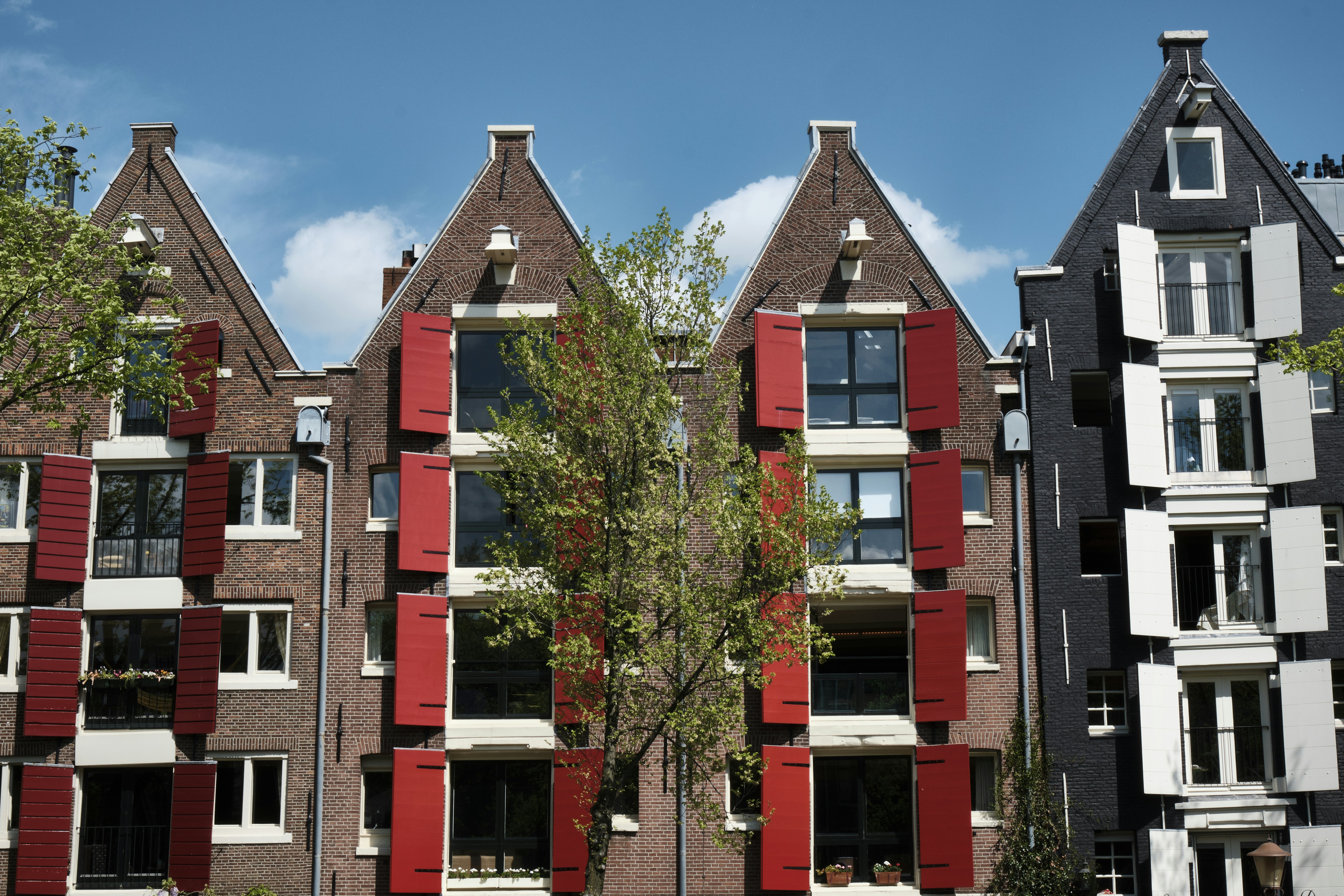 Gabled brick buildings with red and white shutters under a bright blue sky.