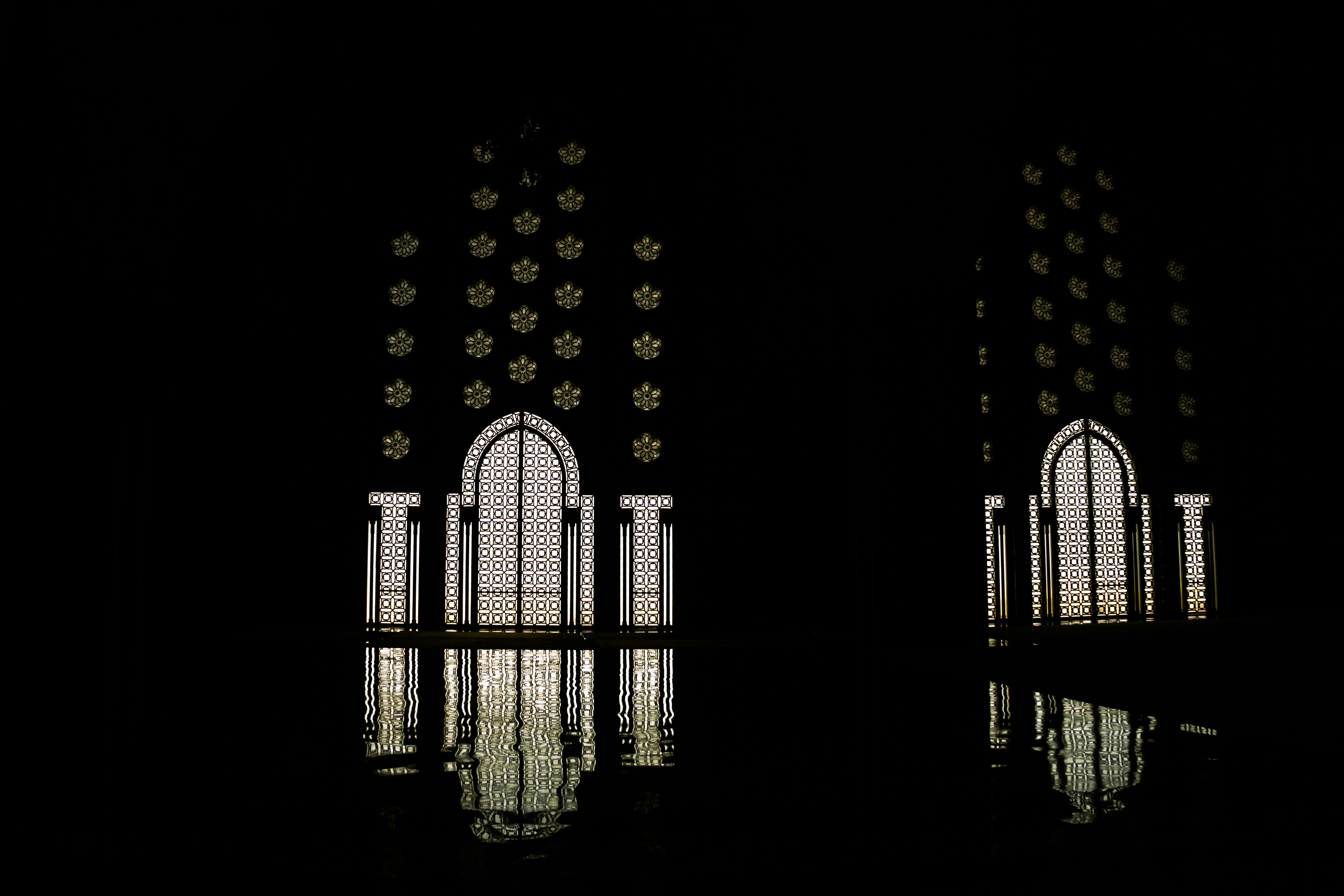 Intricate patterned arches illuminated against a dark backdrop, reflecting in still water below.