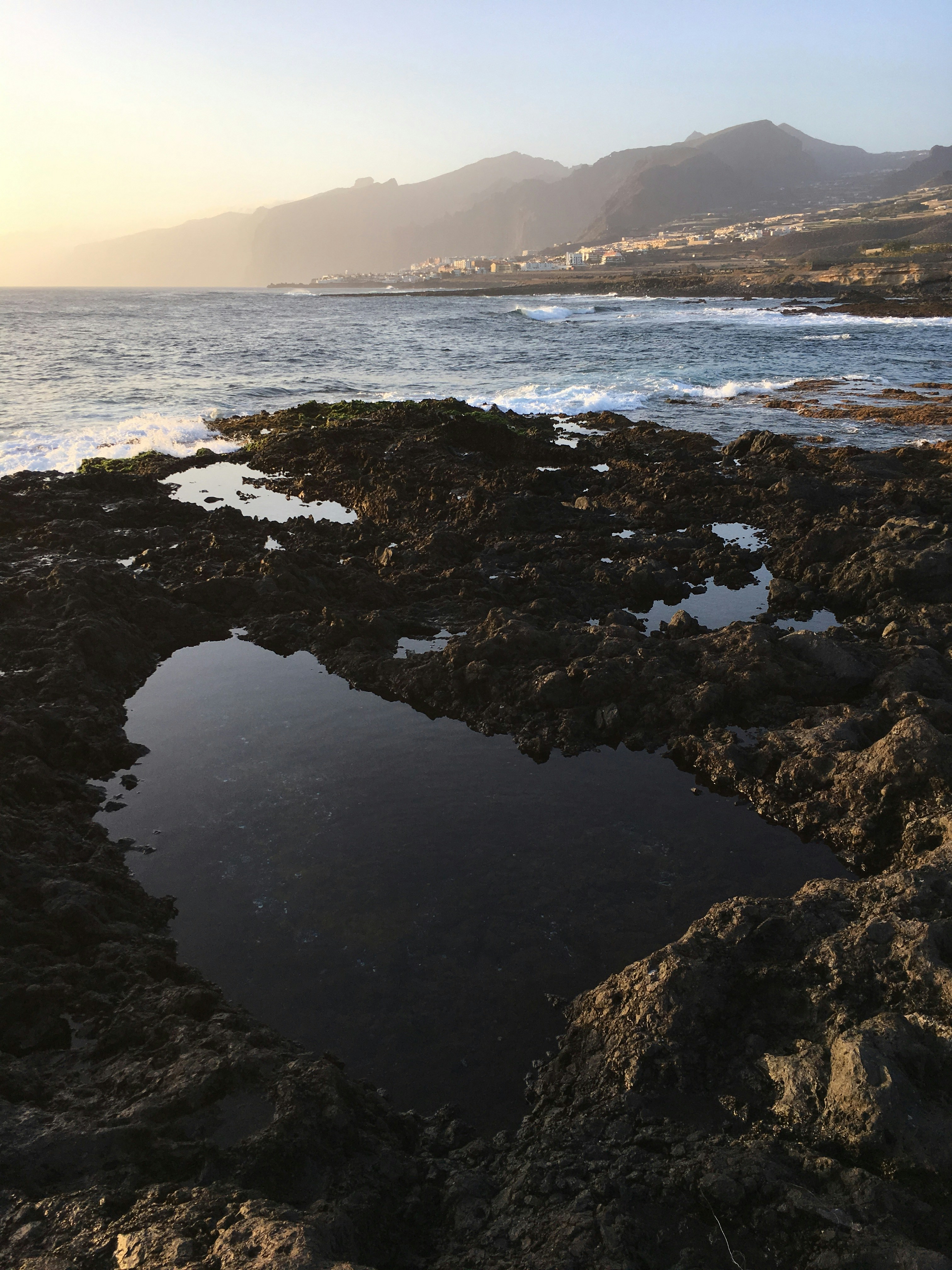 Lava-strewn shoreline at sunset with distant coastal town