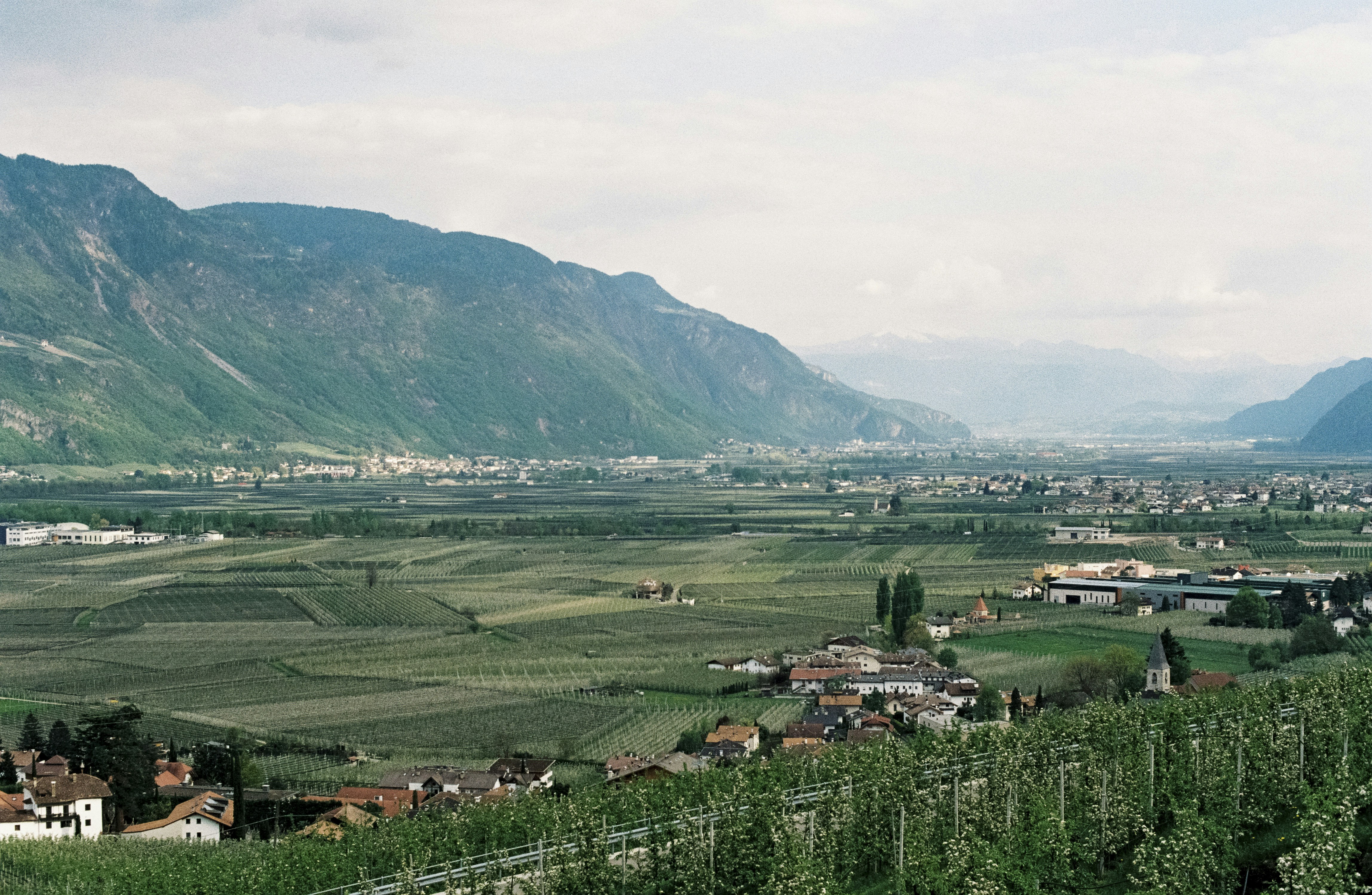 Expansive valley with scattered farms and distant mountains under a cloudy sky.