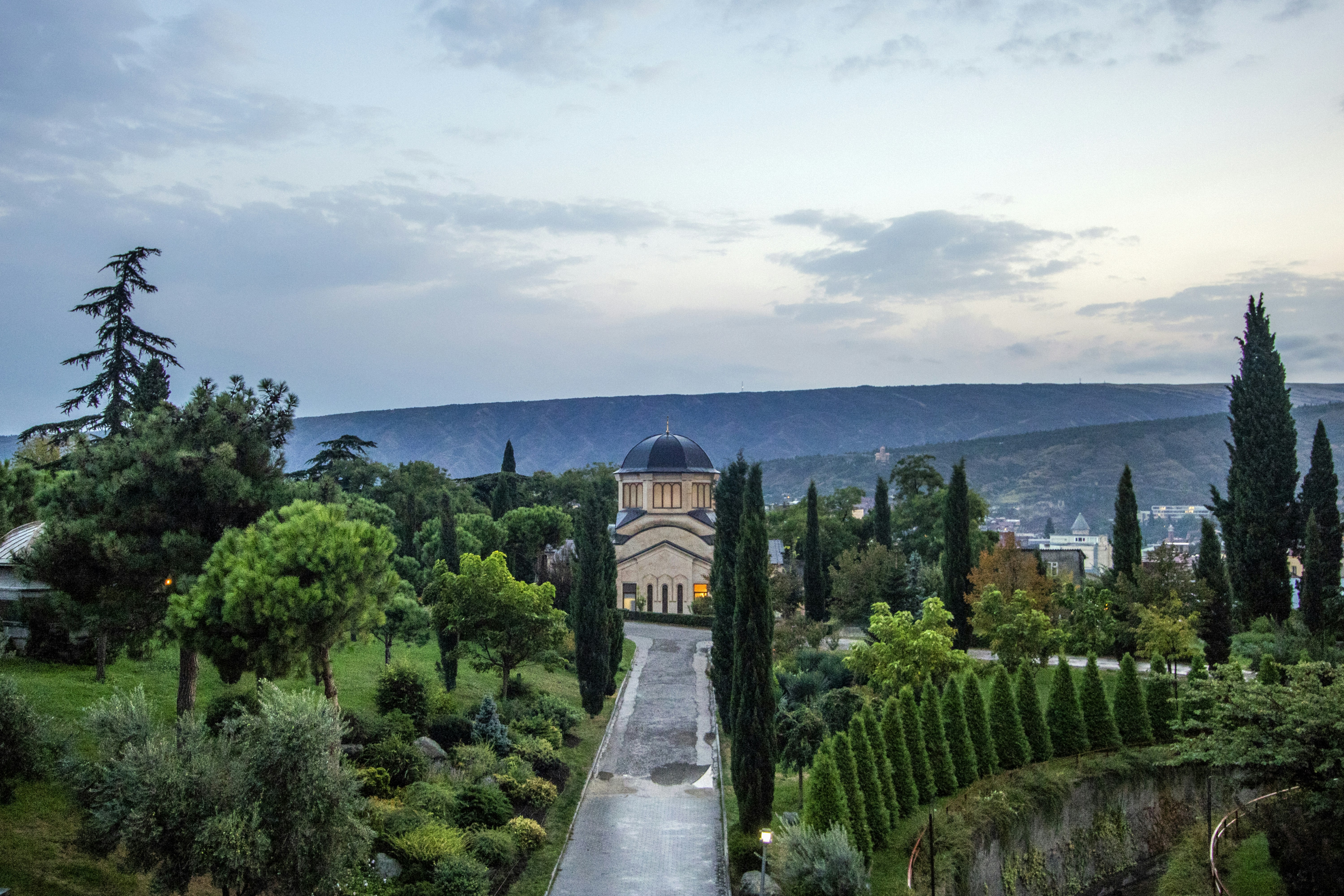 Dome-topped building surrounded by lush greenery and a winding path at dusk.