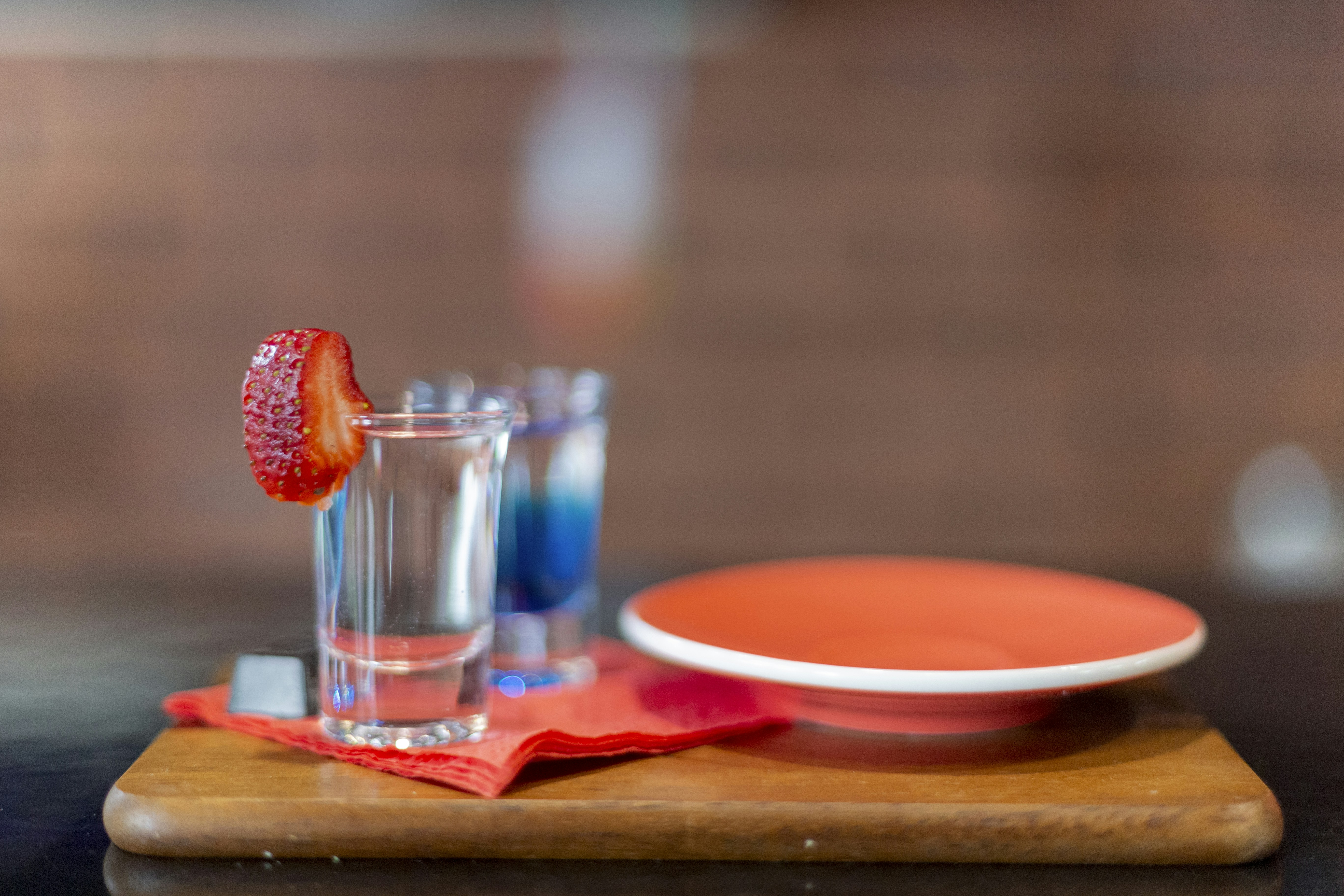 Strawberry Crown on a Glass: A Quiet Barboard Moment with Warm Wood and Blue Backdrop