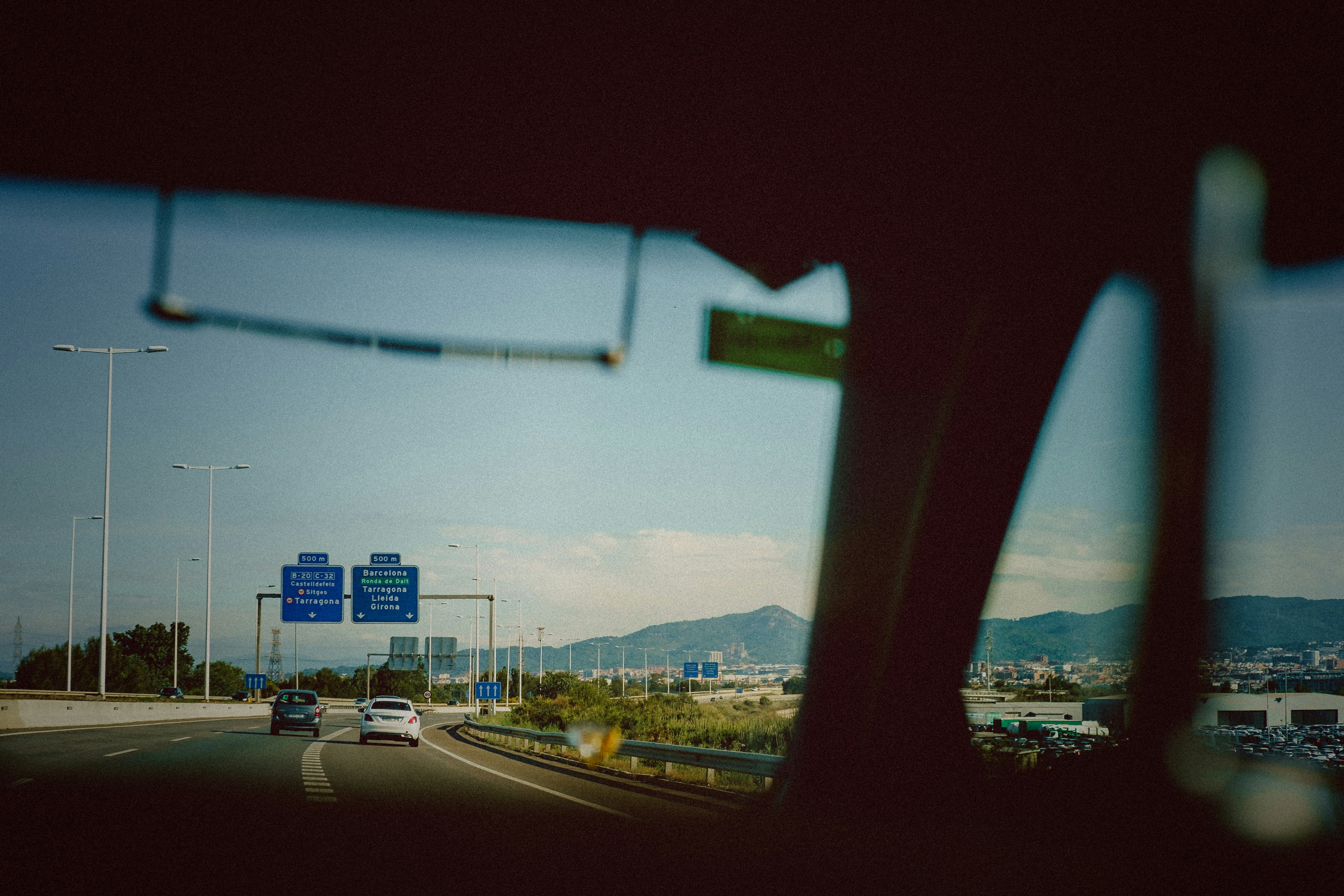 View of a highway from inside a vehicle, showcasing road signs and distant mountains under a clear sky.