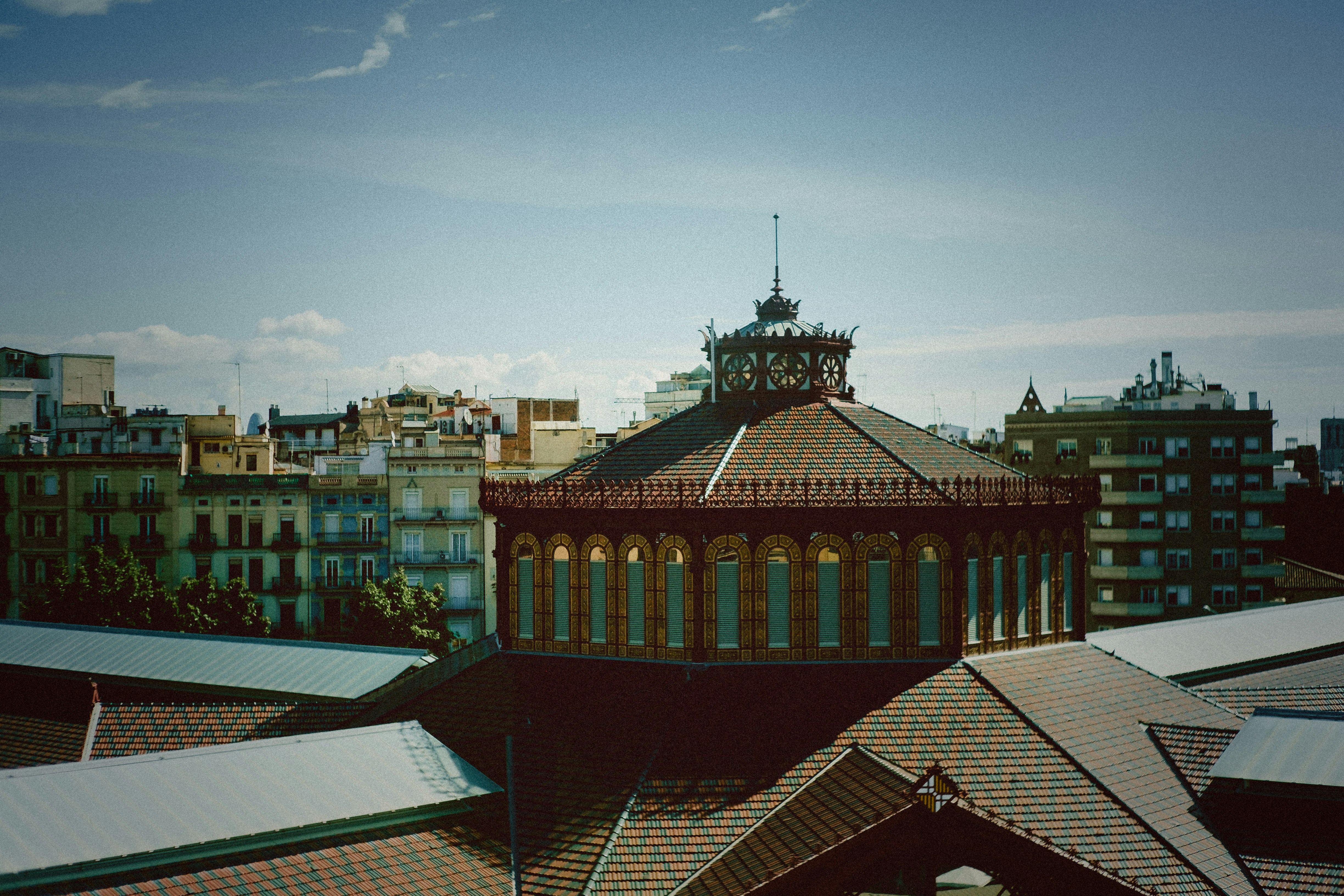 Historic roof structure with intricate detailing set against a vibrant city skyline under a clear blue sky.