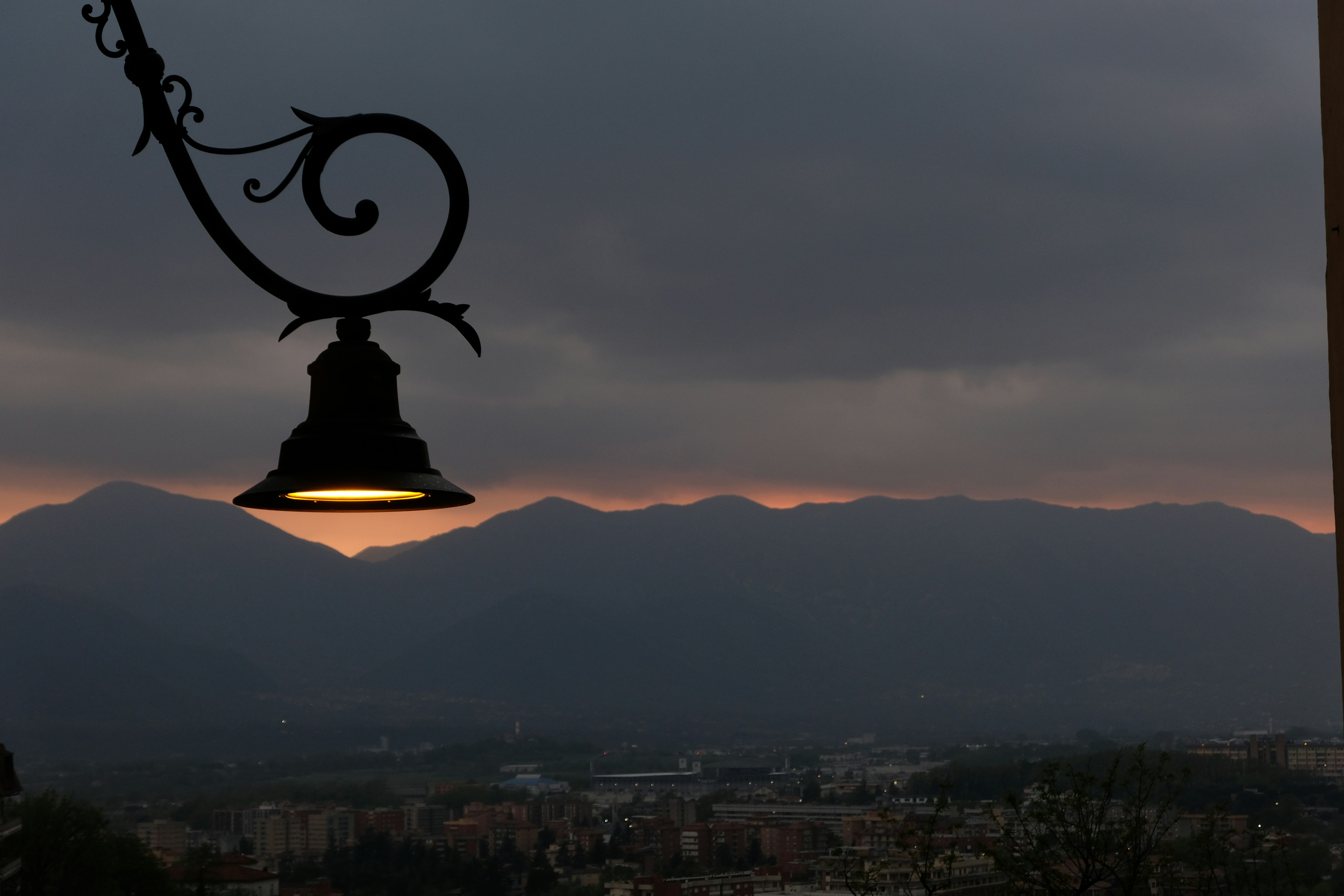 Ornate street lamp illuminating against a backdrop of mountains at sunset.
