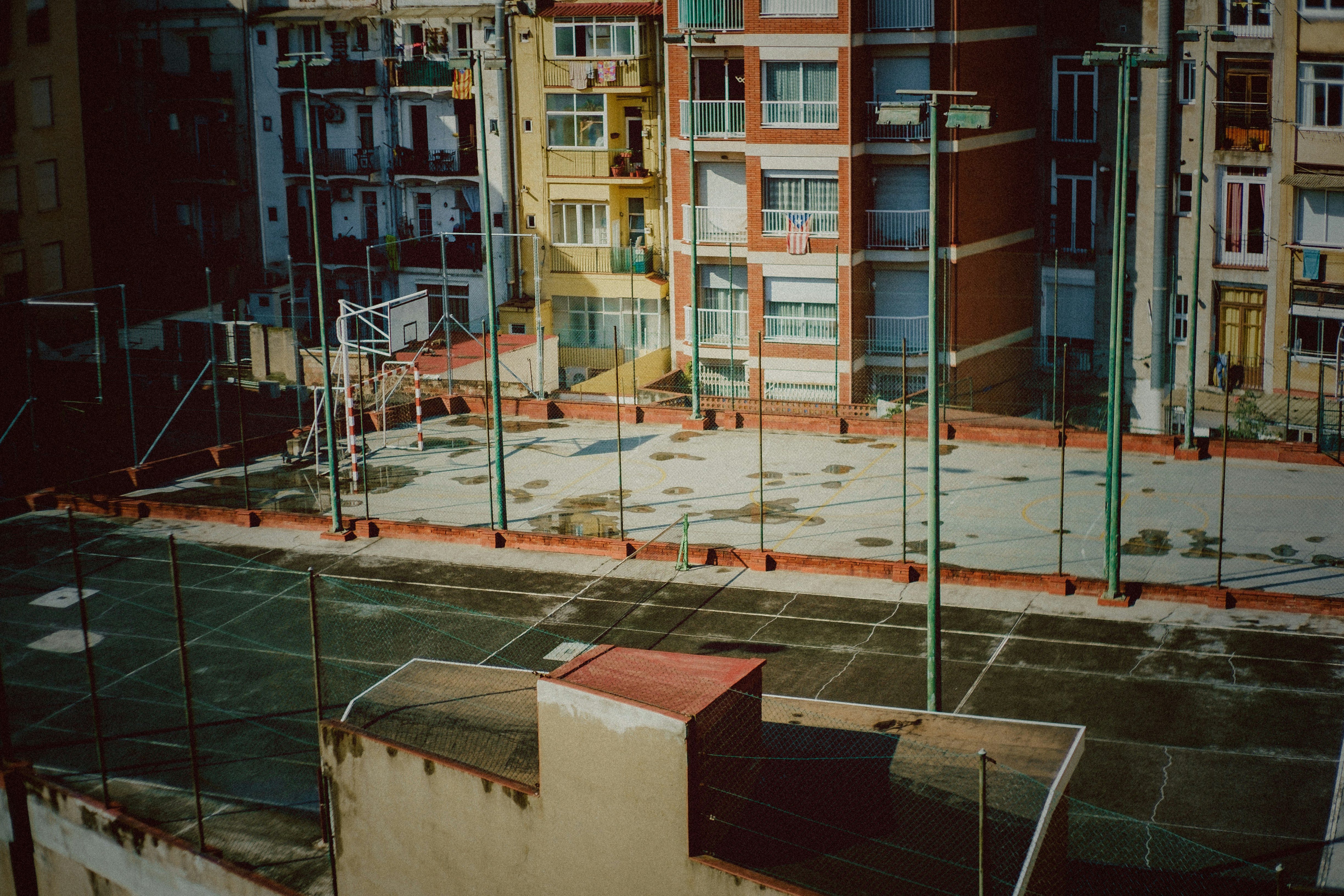 Abandoned sports court surrounded by residential buildings, showcasing worn-out surfaces and a sense of solitude.
