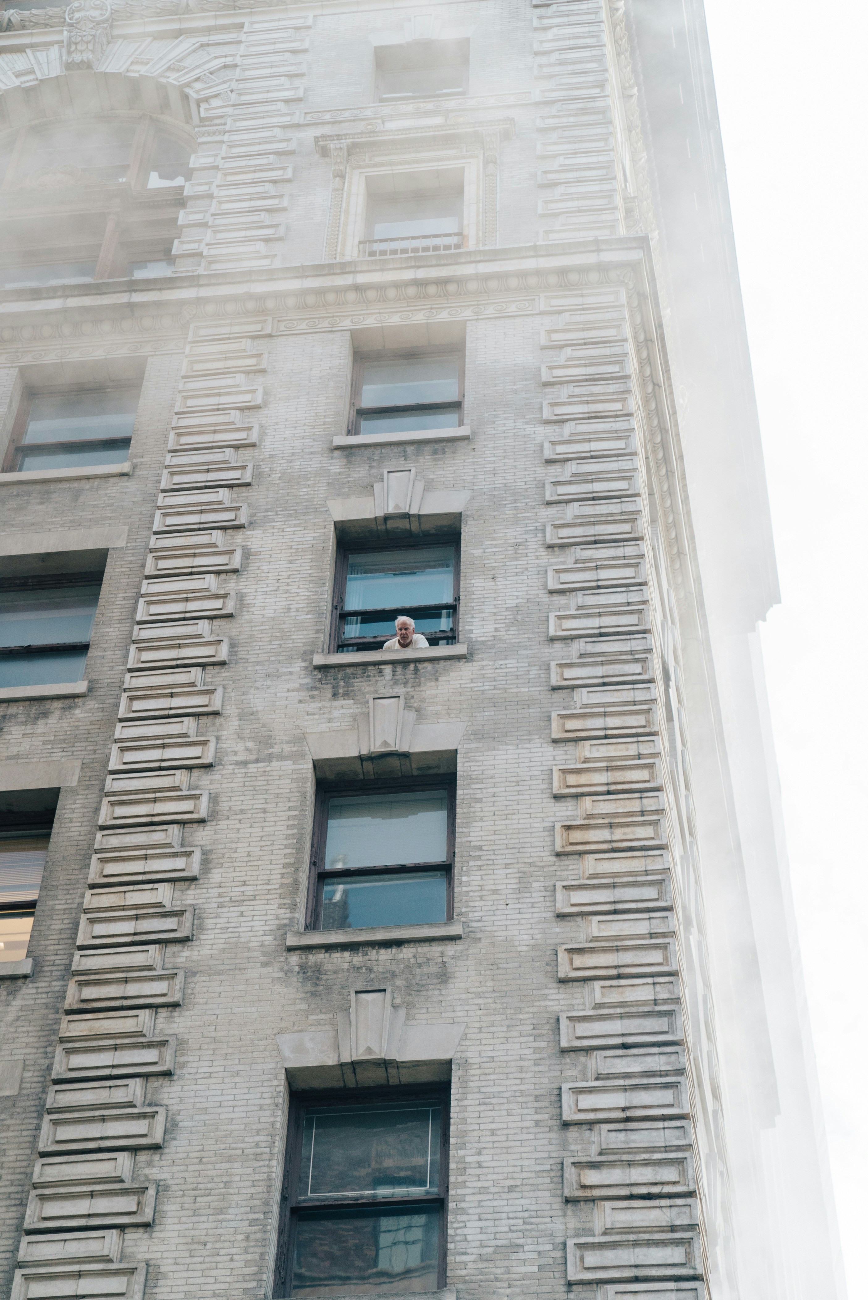 Lone Figure at a Mid-Rise Window Against a Pale Brick Facade