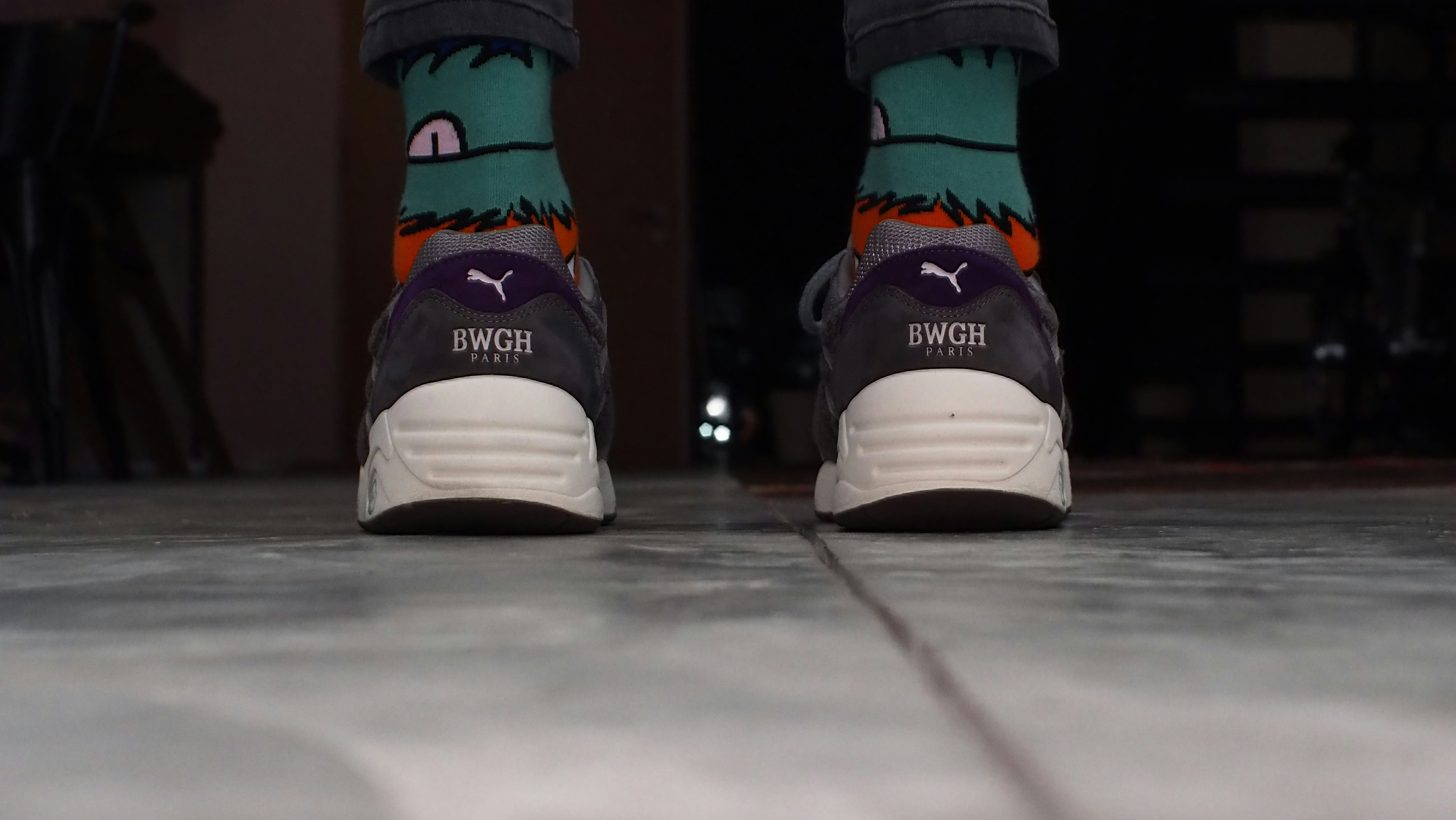 Colorful socks paired with sneakers on a tiled floor, viewed from the back.